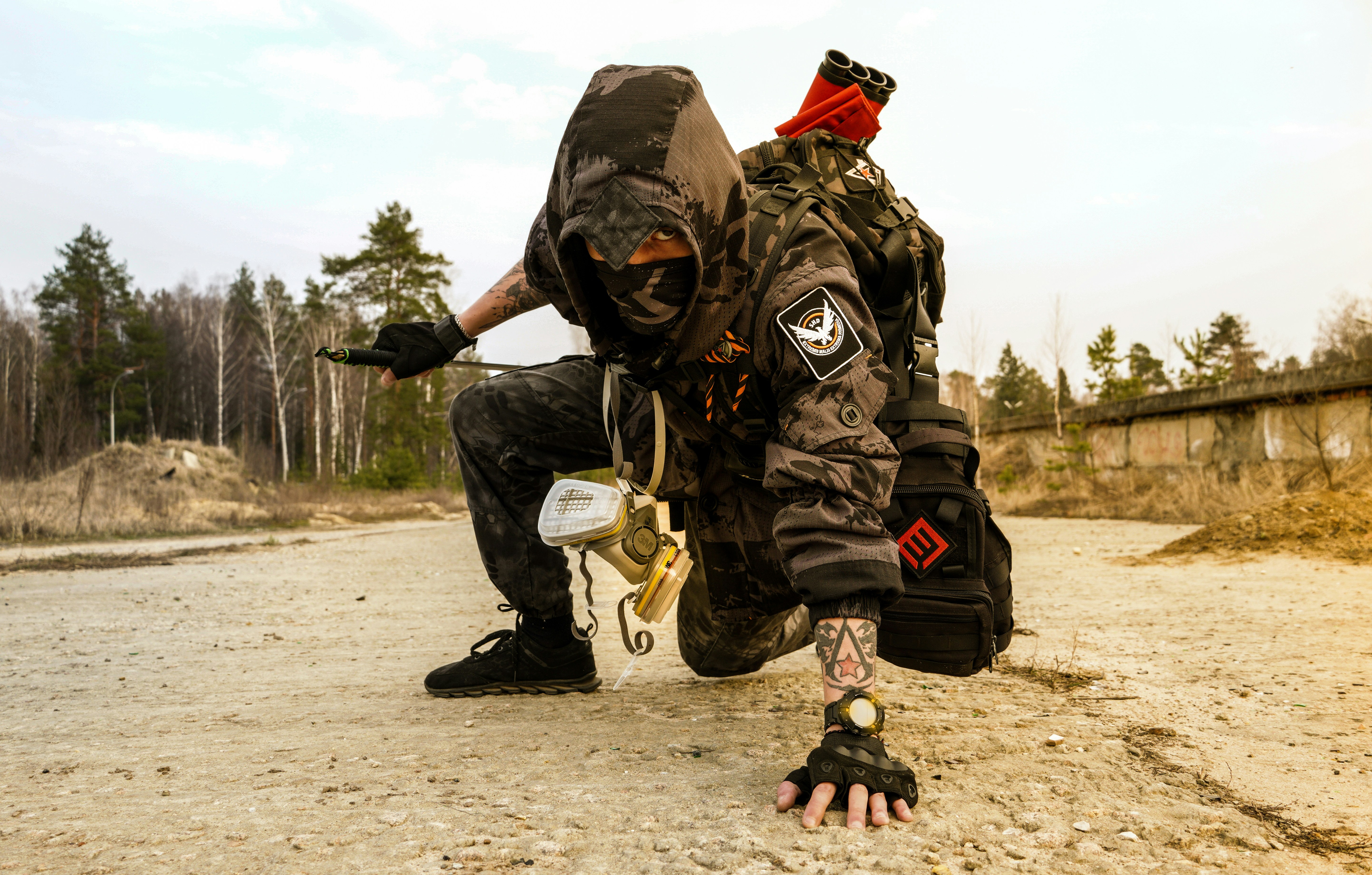 A figure in a tactical outfit crouches in an abandoned landscape, equipped with a gas mask and survival gear, embodying resilience in a desolate environment.