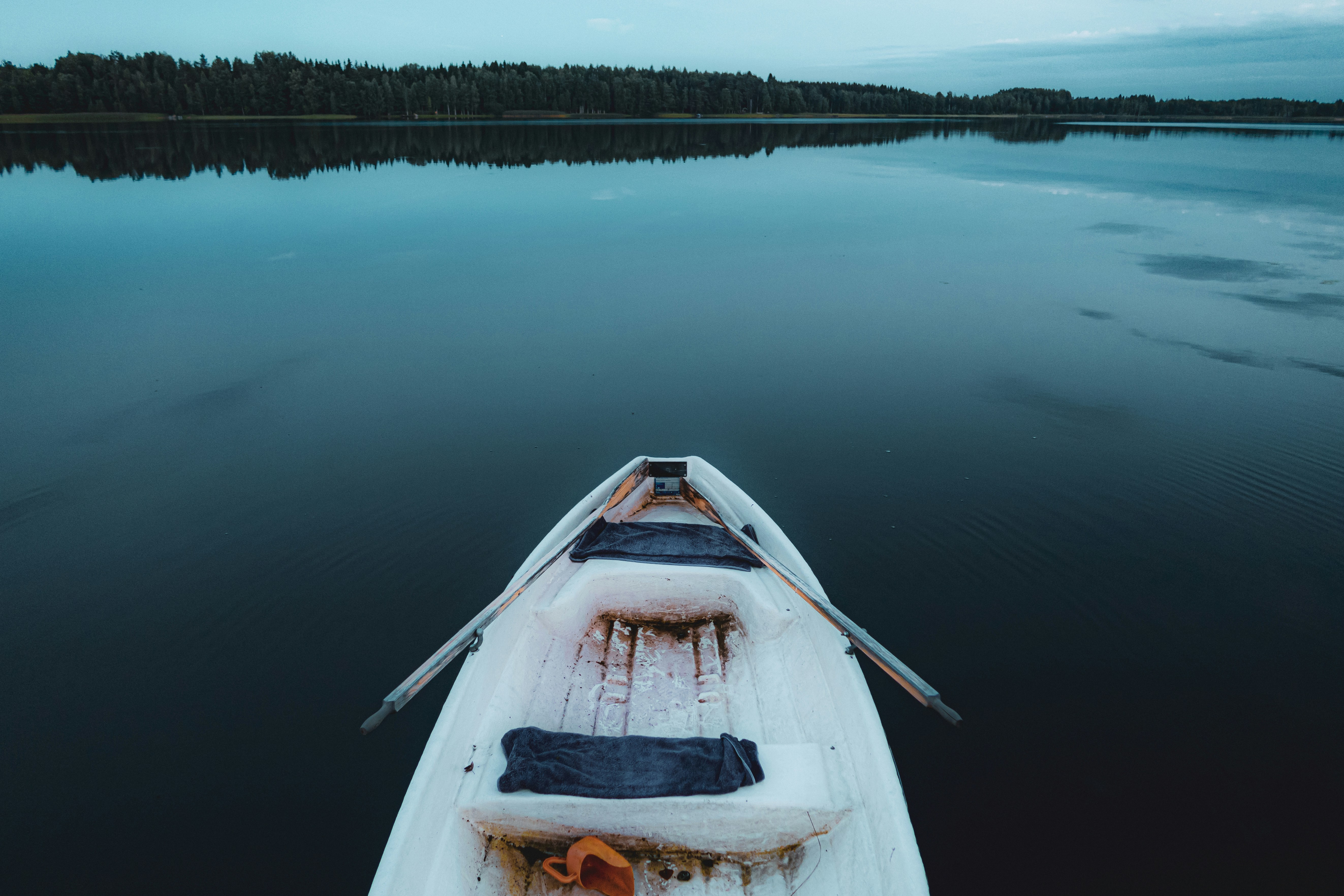 A weathered rowboat rests on calm waters, reflecting the tranquil sky and surrounding forest. The scene captures a moment of peace and solitude.