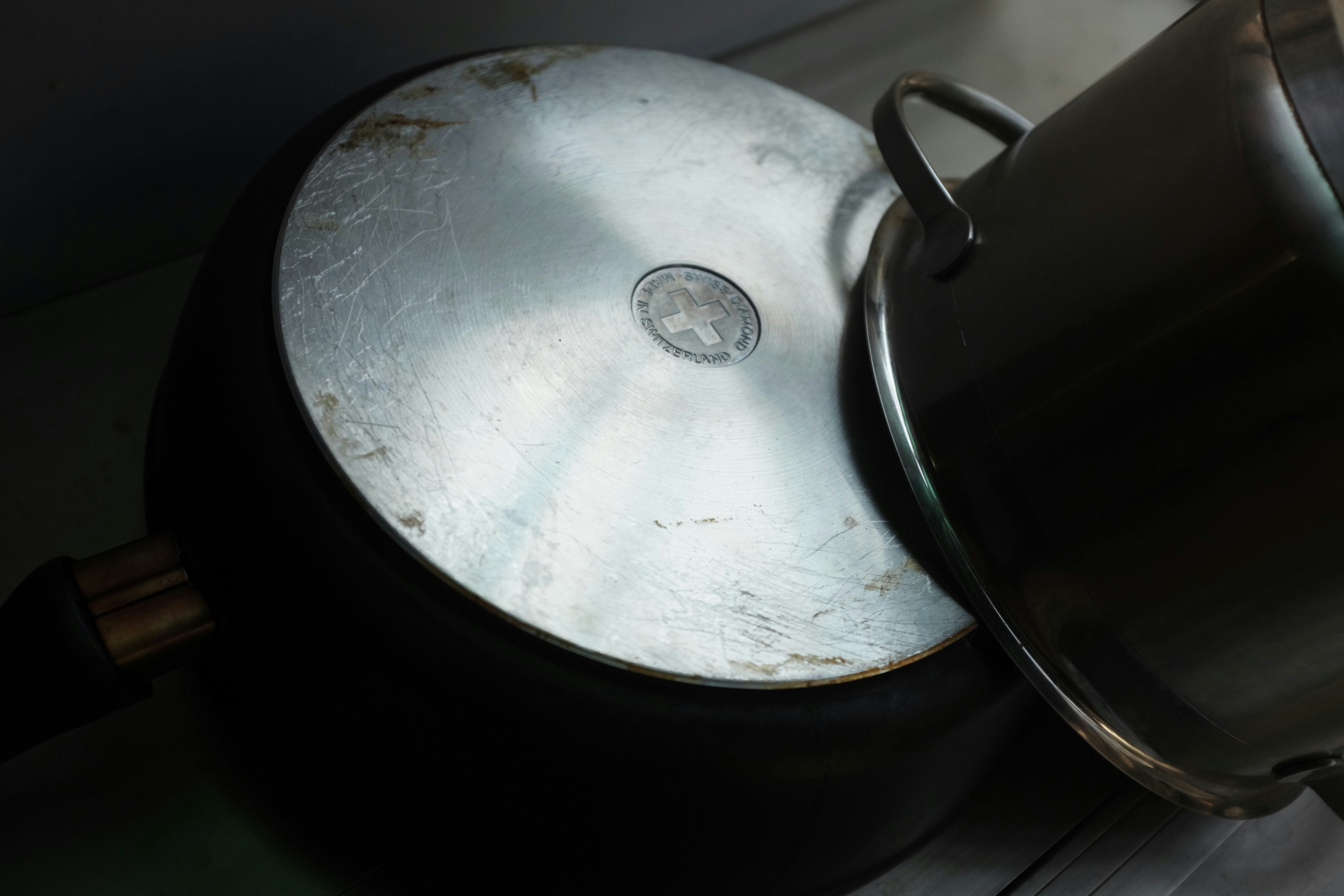 A stainless steel pot resting on a black frying pan, highlighting the interplay of light and texture in a kitchen setting.