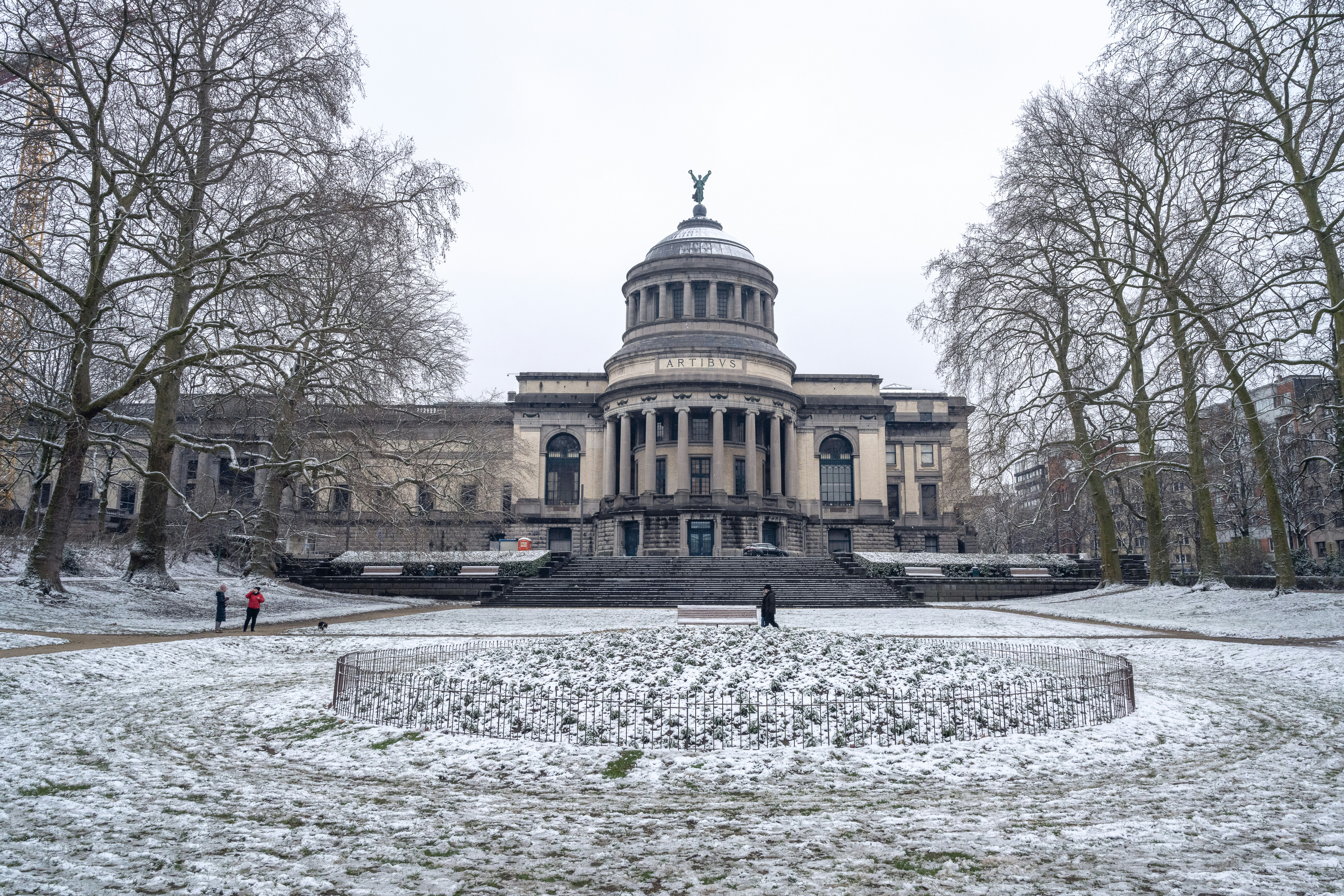 Grand neoclassical building with a domed roof surrounded by snow-covered trees and grounds.