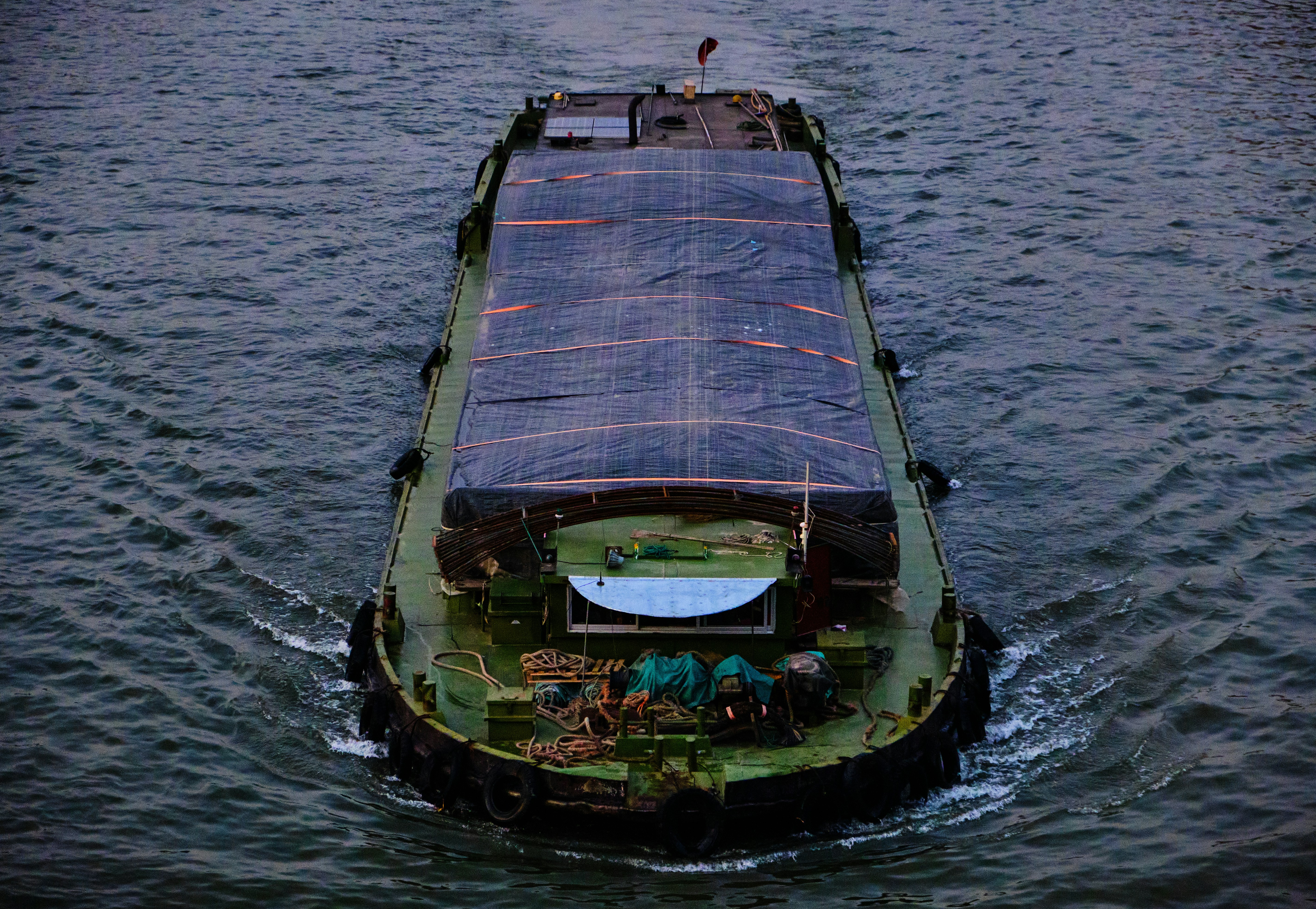 A solitary barge traverses a quiet harbor under a slate-gray sky