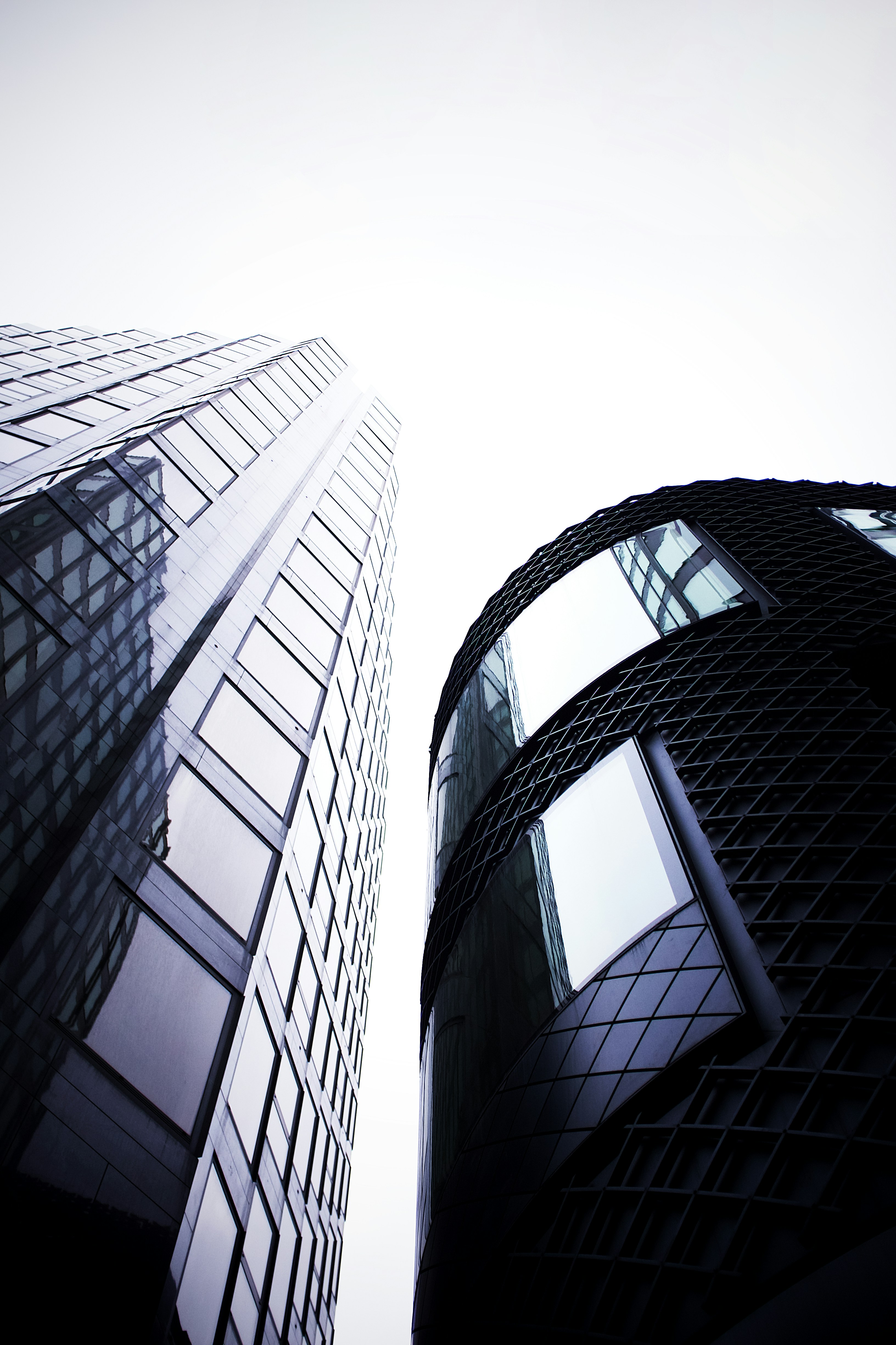 Two modern skyscrapers captured from below, showcasing their sleek lines and reflective surfaces against a pale sky.