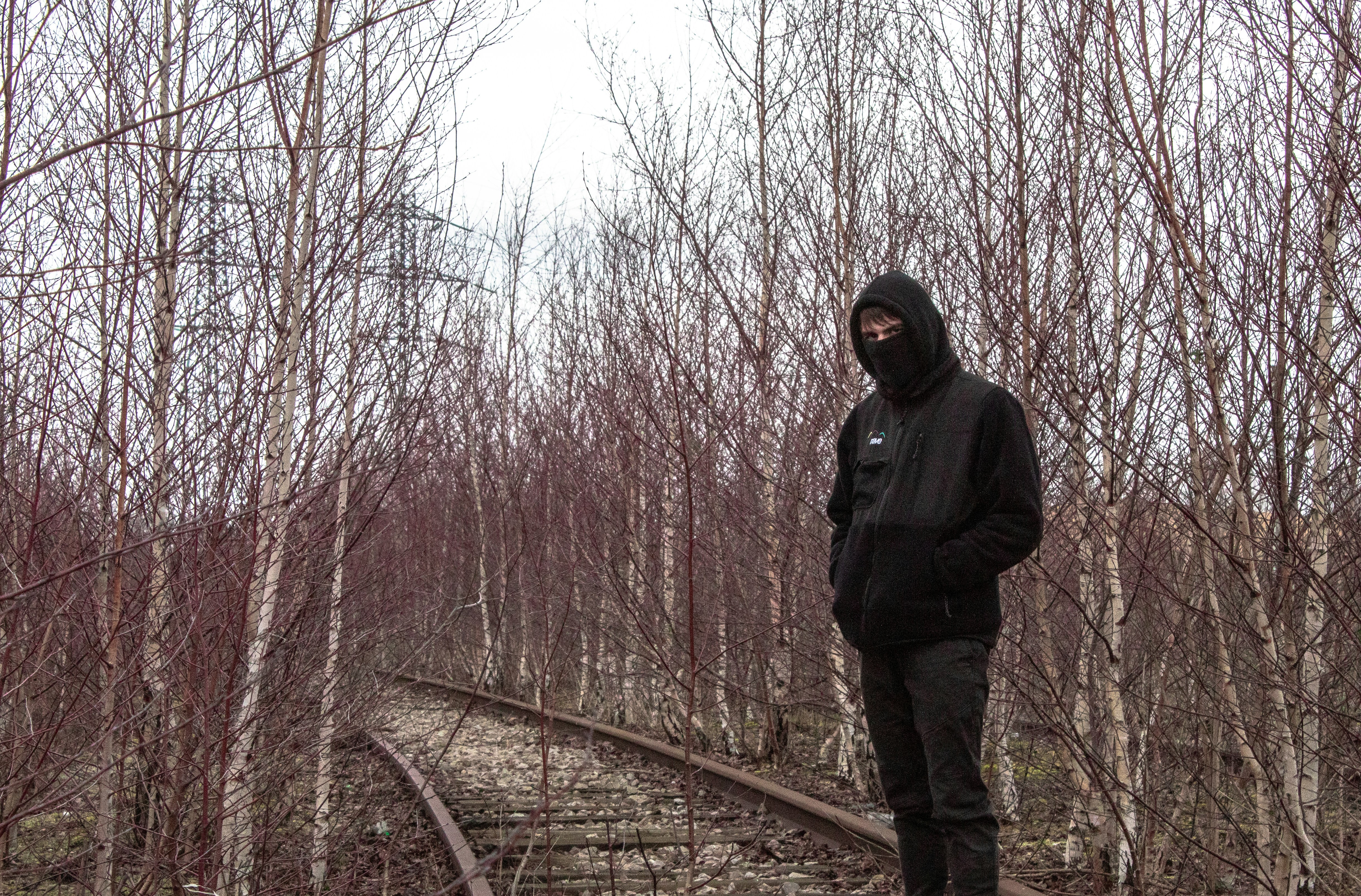 Hooded Figure on Abandoned Tracks Amid Winter Trees