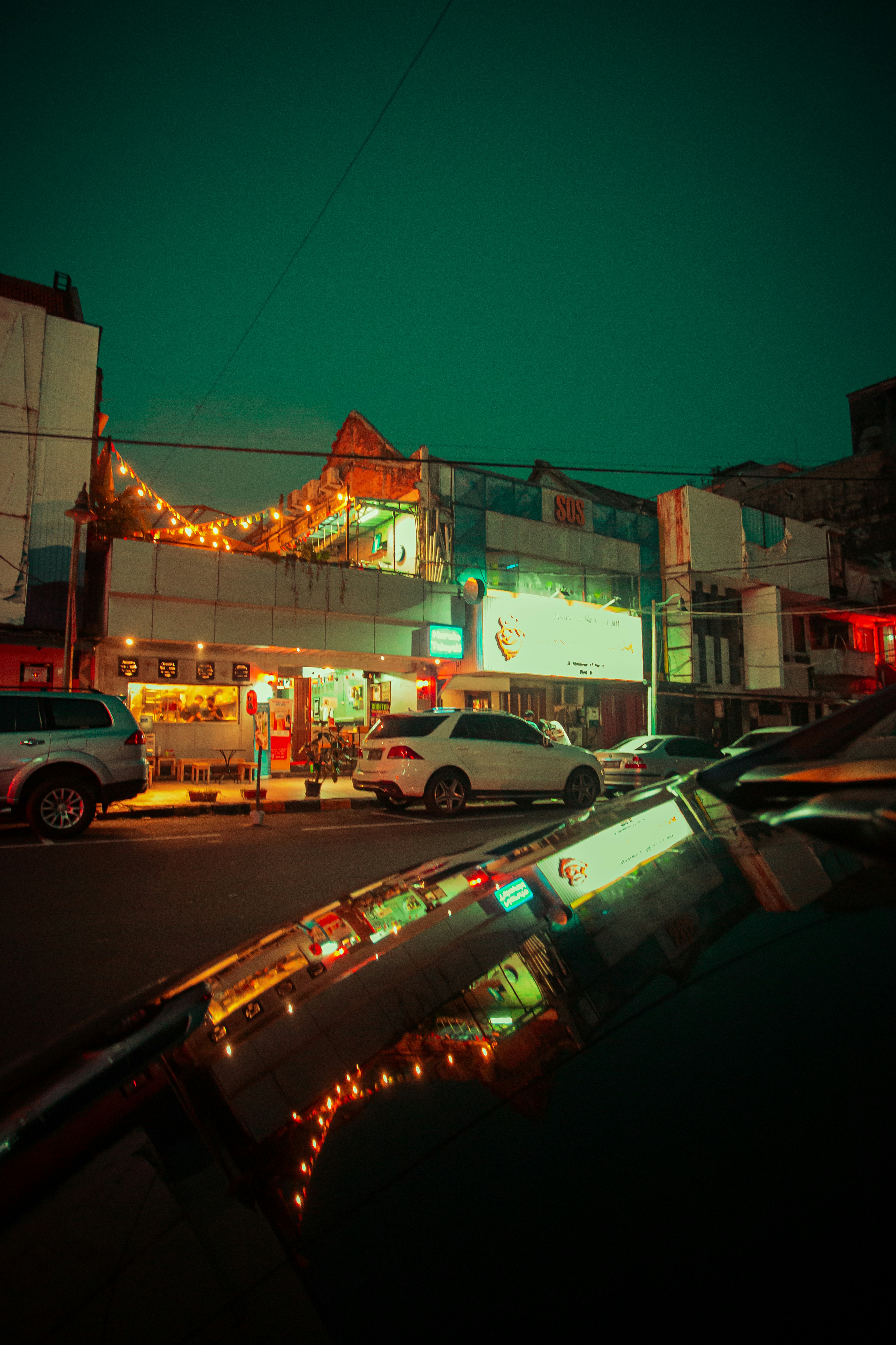 Neon Strings over a Quiet Street: Night Market Reflections on a Gleaming Hood