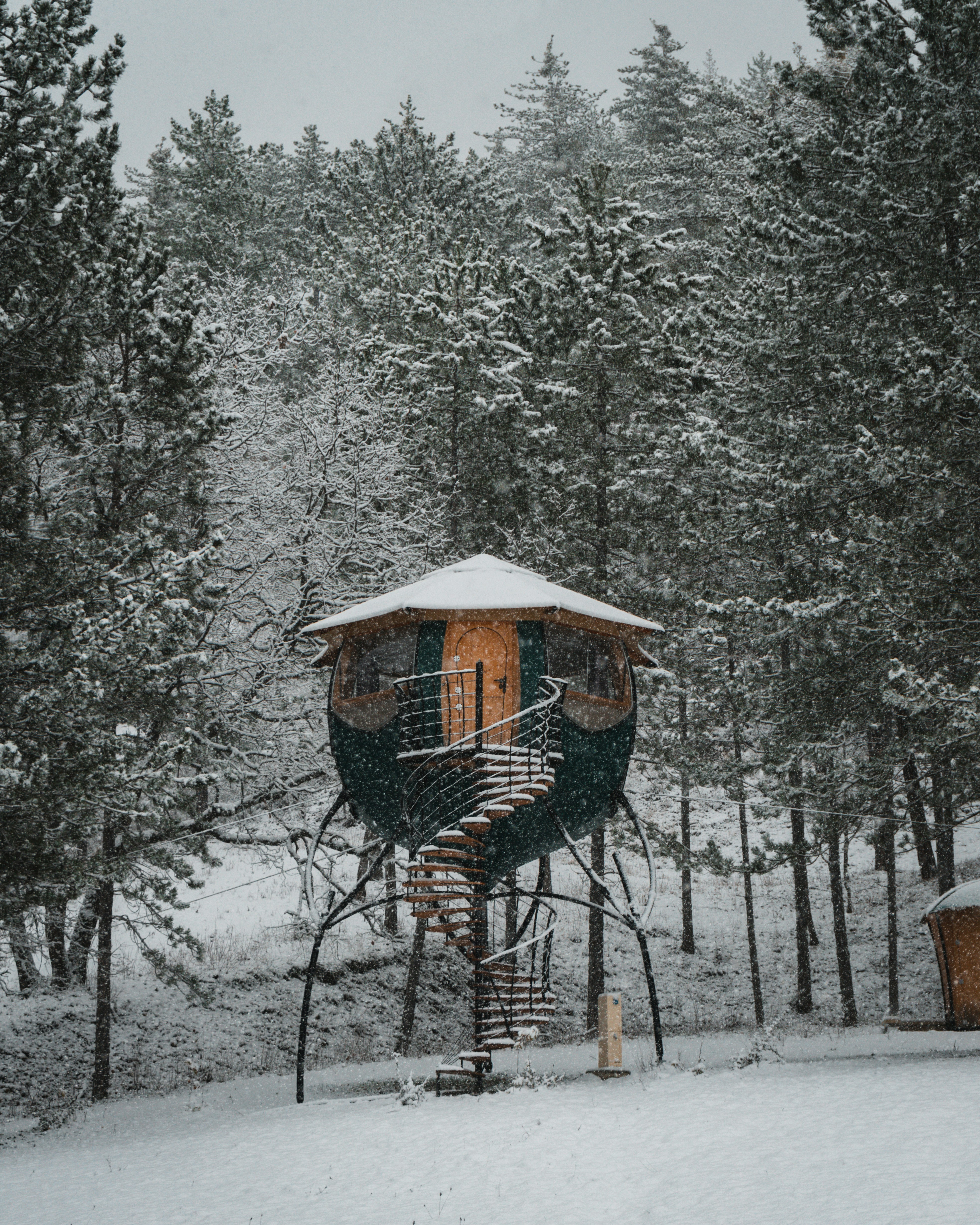 A whimsical treehouse with a spiral staircase, surrounded by a snowy forest landscape, creating a serene winter getaway.