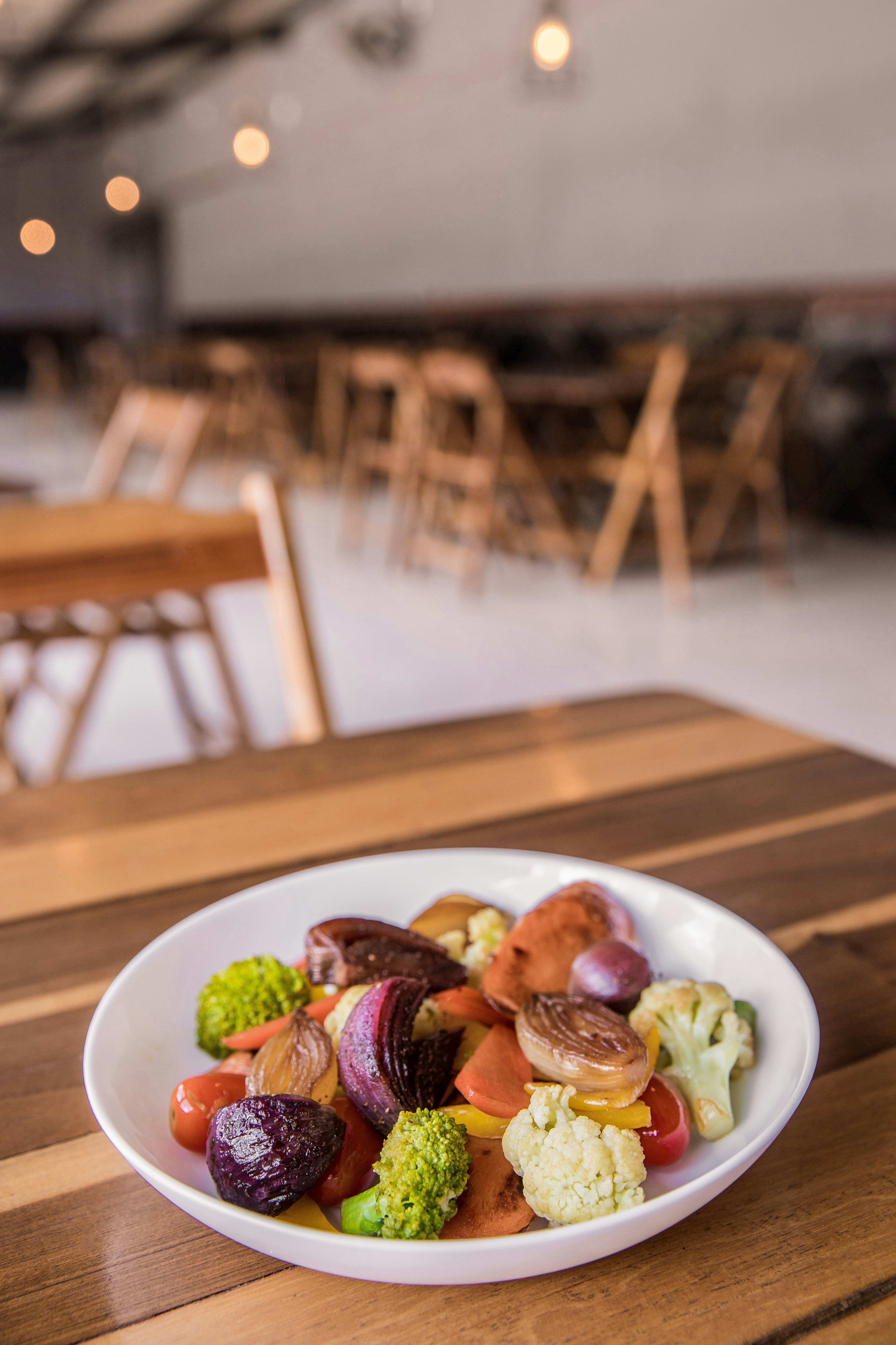 Colorful bowl of roasted vegetables on a wooden table in a softly lit cafe