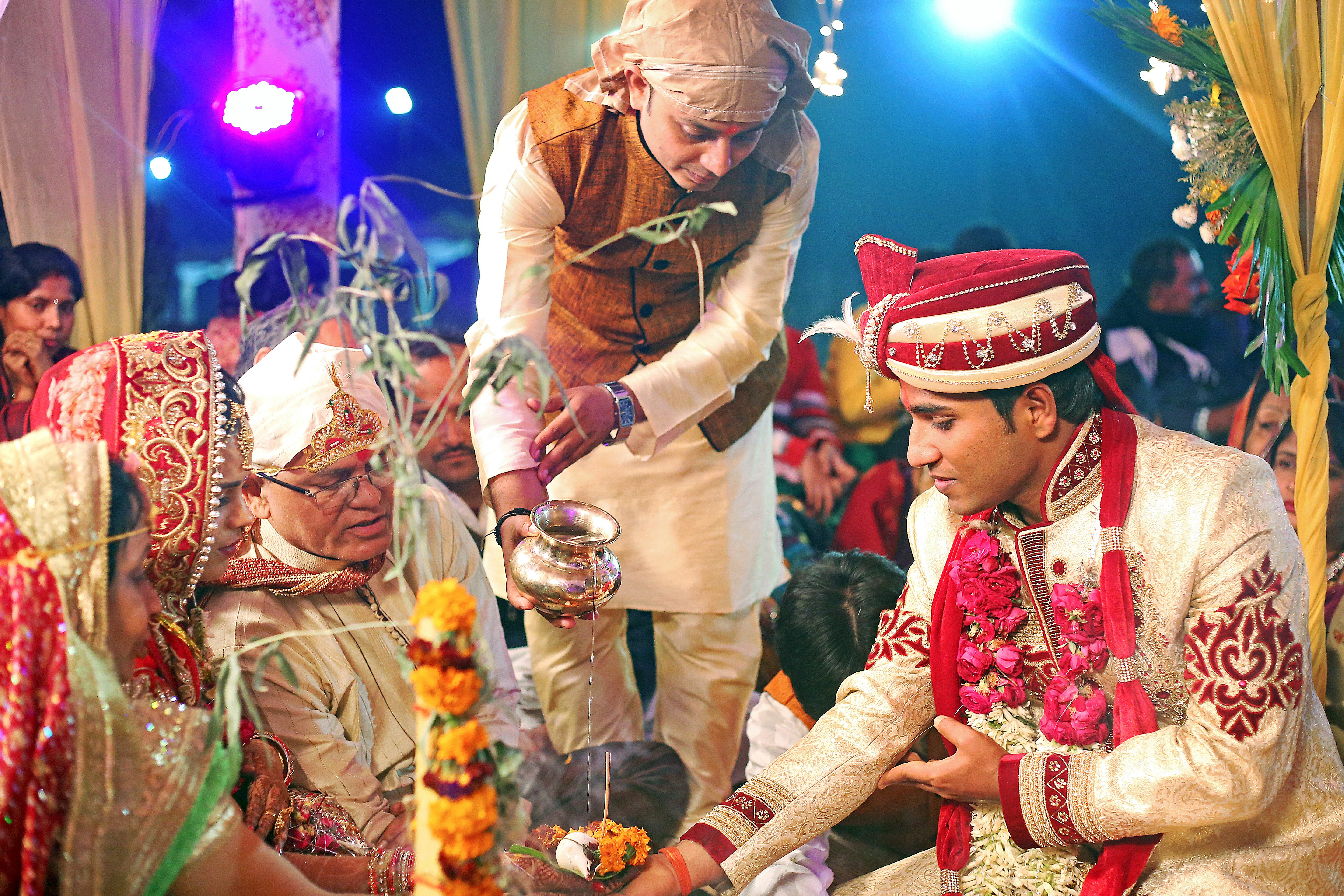 Traditional wedding ceremony with participants in ornate attire under vibrant lighting.