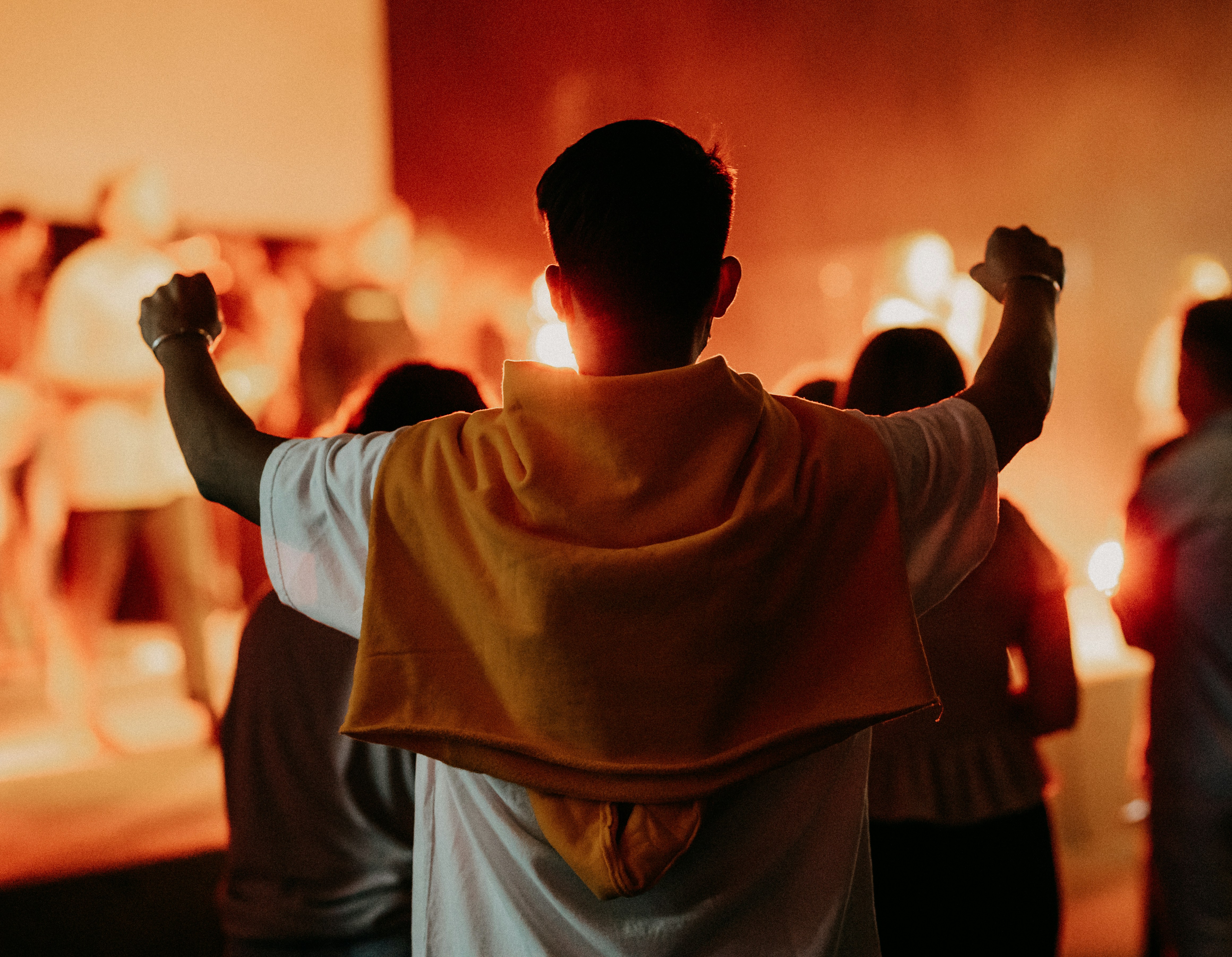 Audience member with arms raised in celebration at a vibrant live event, illuminated by warm stage lights.