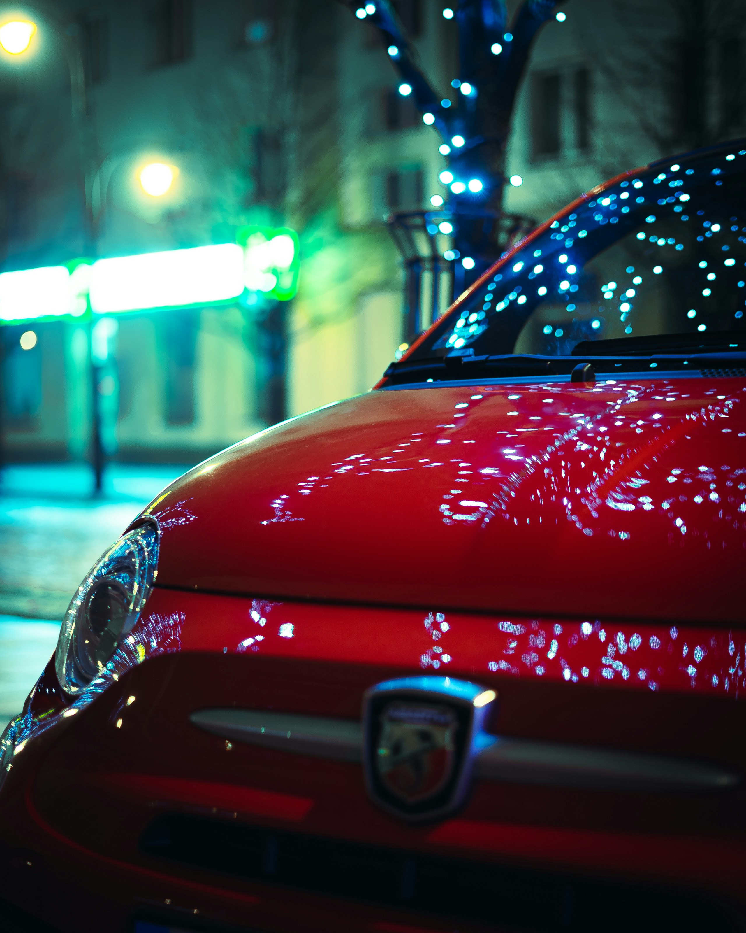 Crimson Hood Under Neon Night: Abarth Emblem Amid City Lights