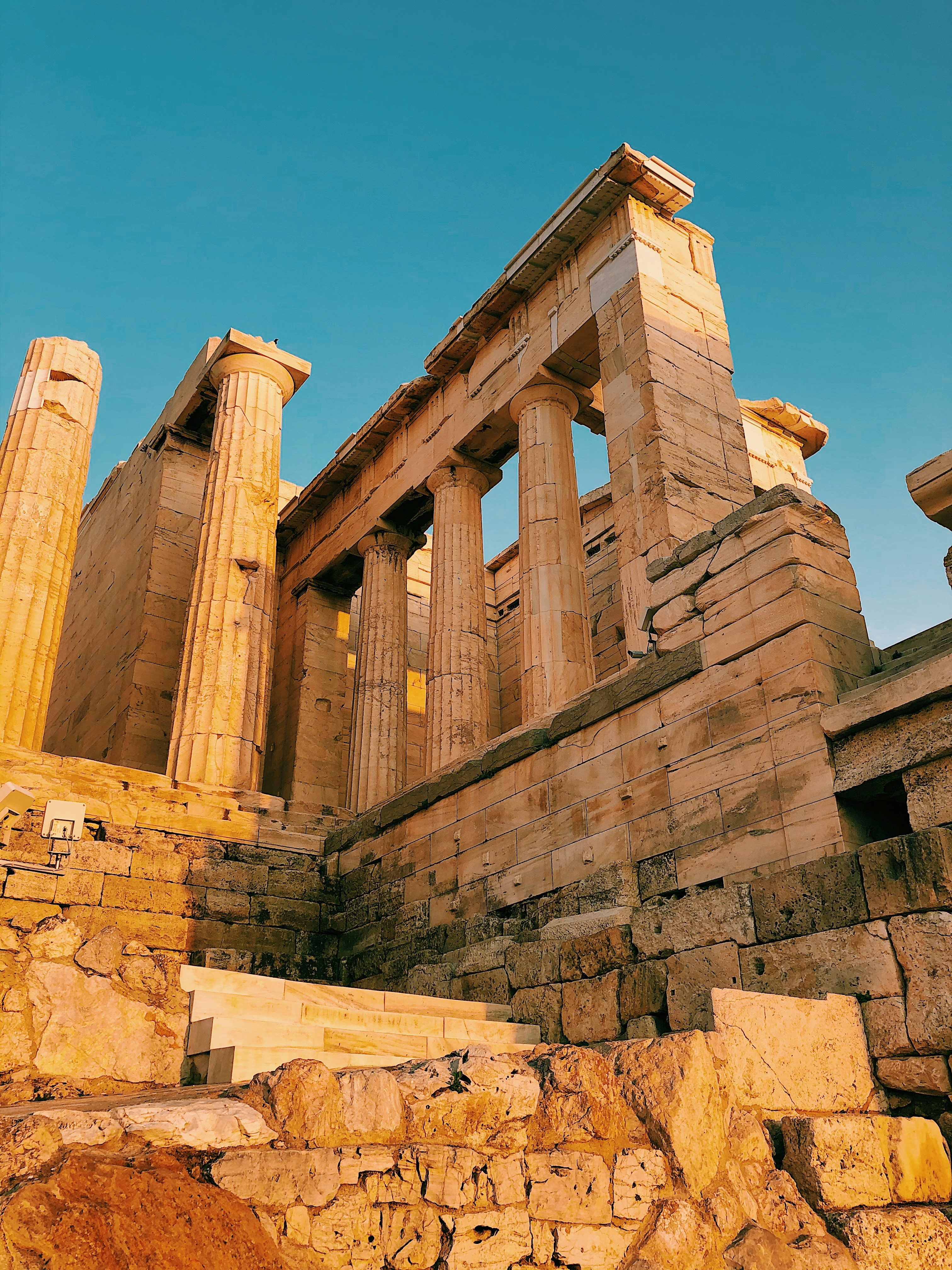 Ancient Greek temple ruins bathed in warm golden light against a clear blue sky.