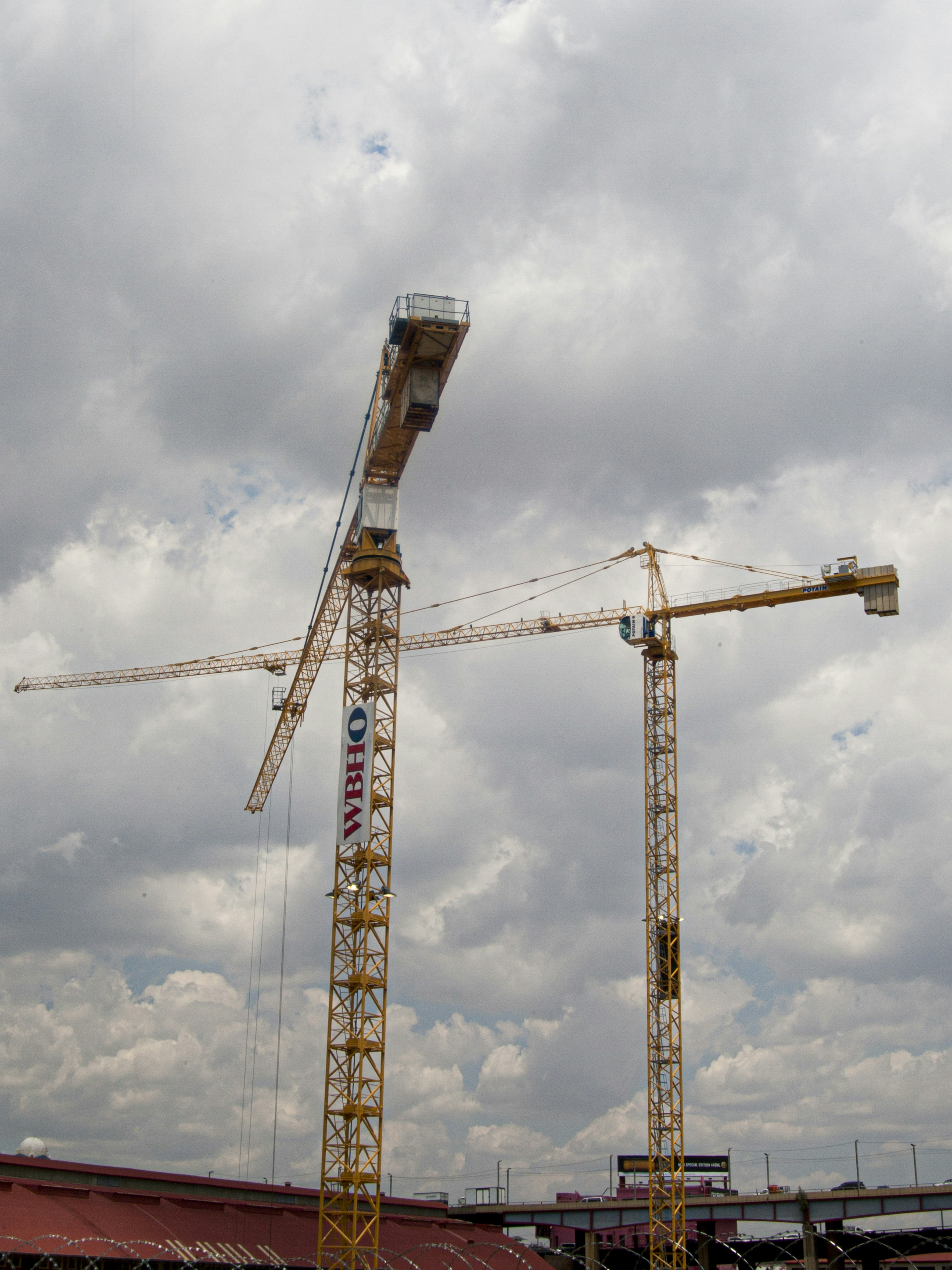 Two towering cranes dominate the skyline, poised against a backdrop of dramatic clouds, symbolizing urban development and progress.