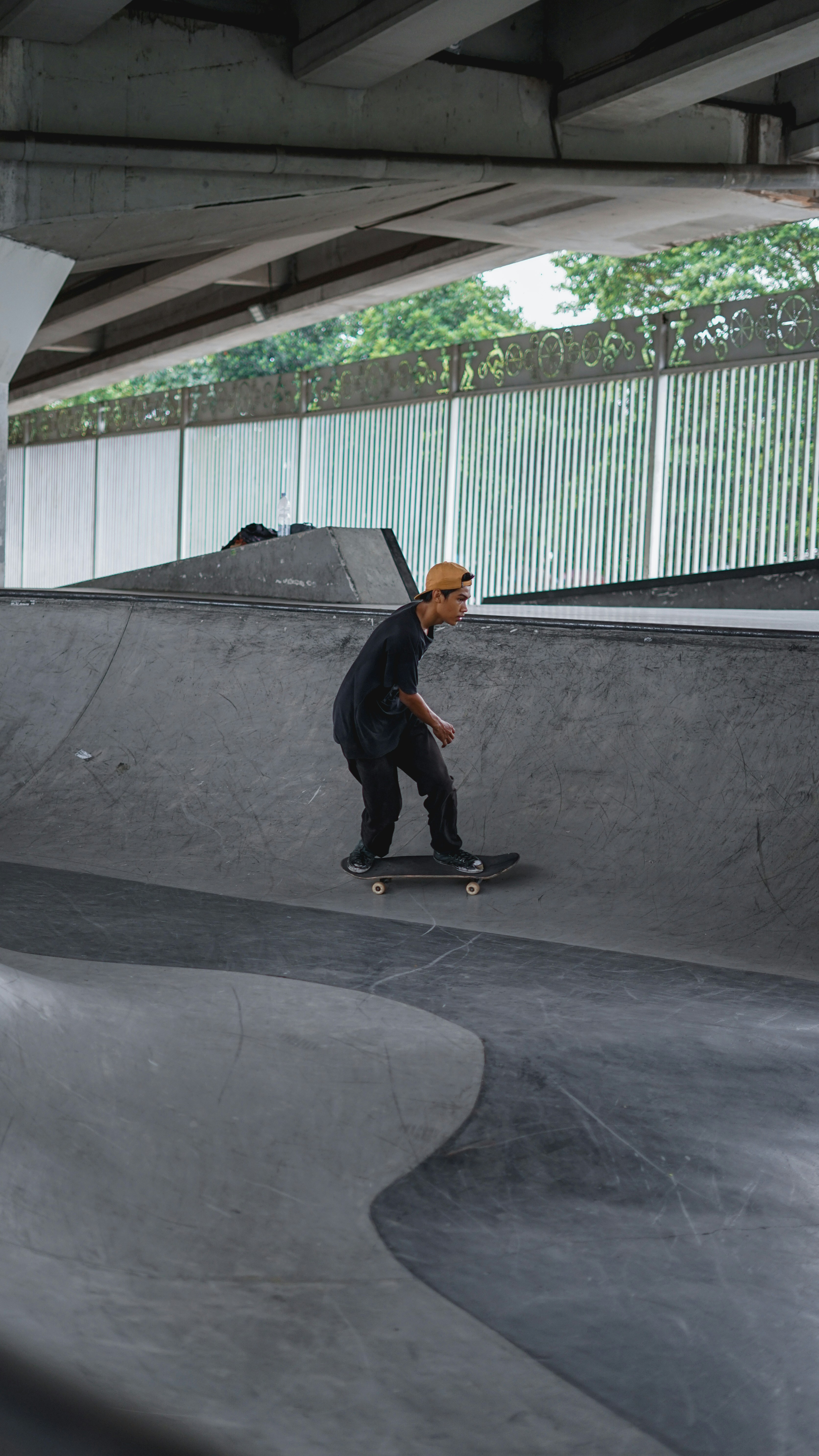 Skateboarder gliding through a modern skate park under a concrete overpass, showcasing agility and style. The scene captures the essence of urban sports culture.
