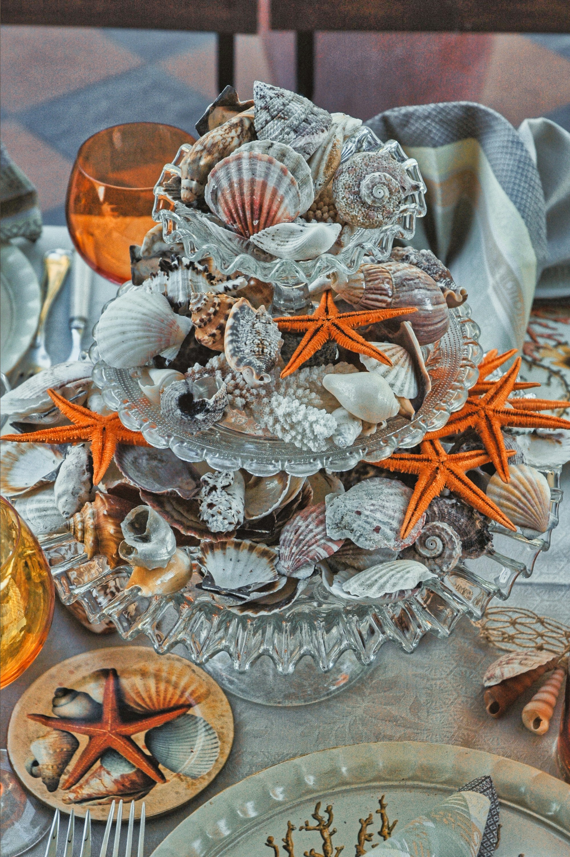 An elegant tiered display of various seashells and starfish, arranged artistically on a dining table, showcasing a coastal theme.