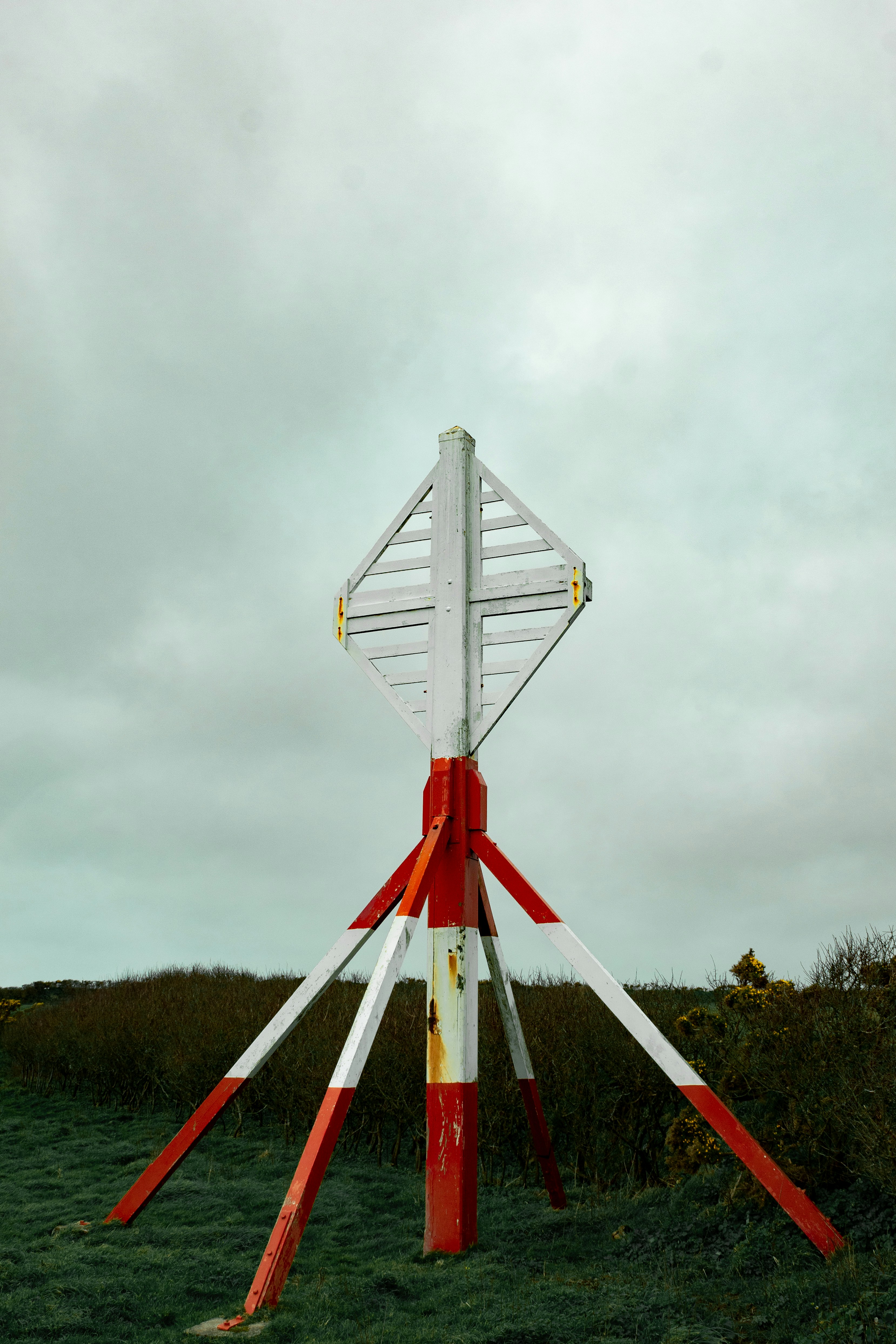 A tall navigational marker stands against a cloudy sky, its red and white paint contrasting with the muted landscape. The structure symbolizes direction and safety.