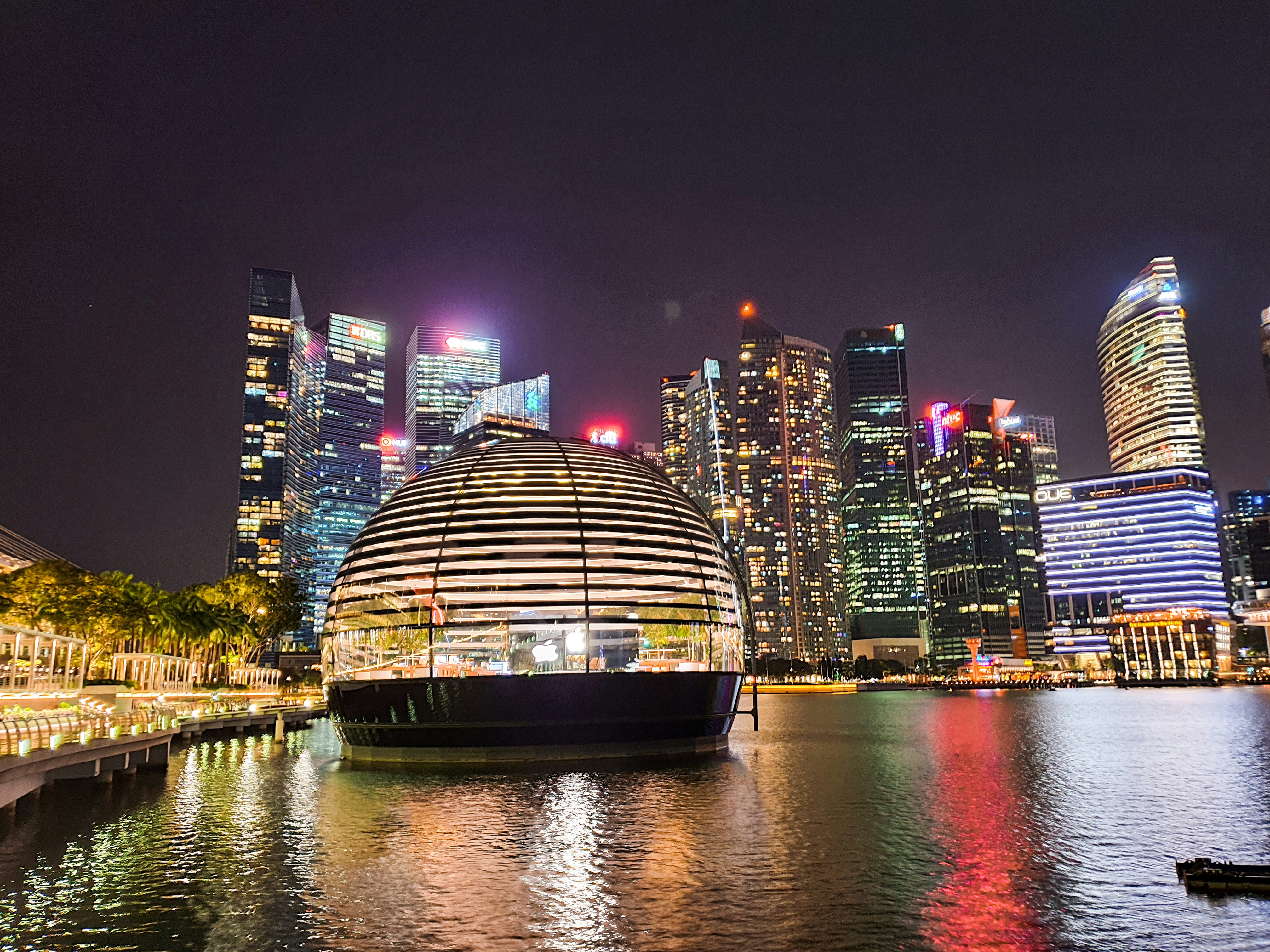 Night cityscape with a glass-domed pavilion floating on calm water, its neon reflections shimmering across the harbor.