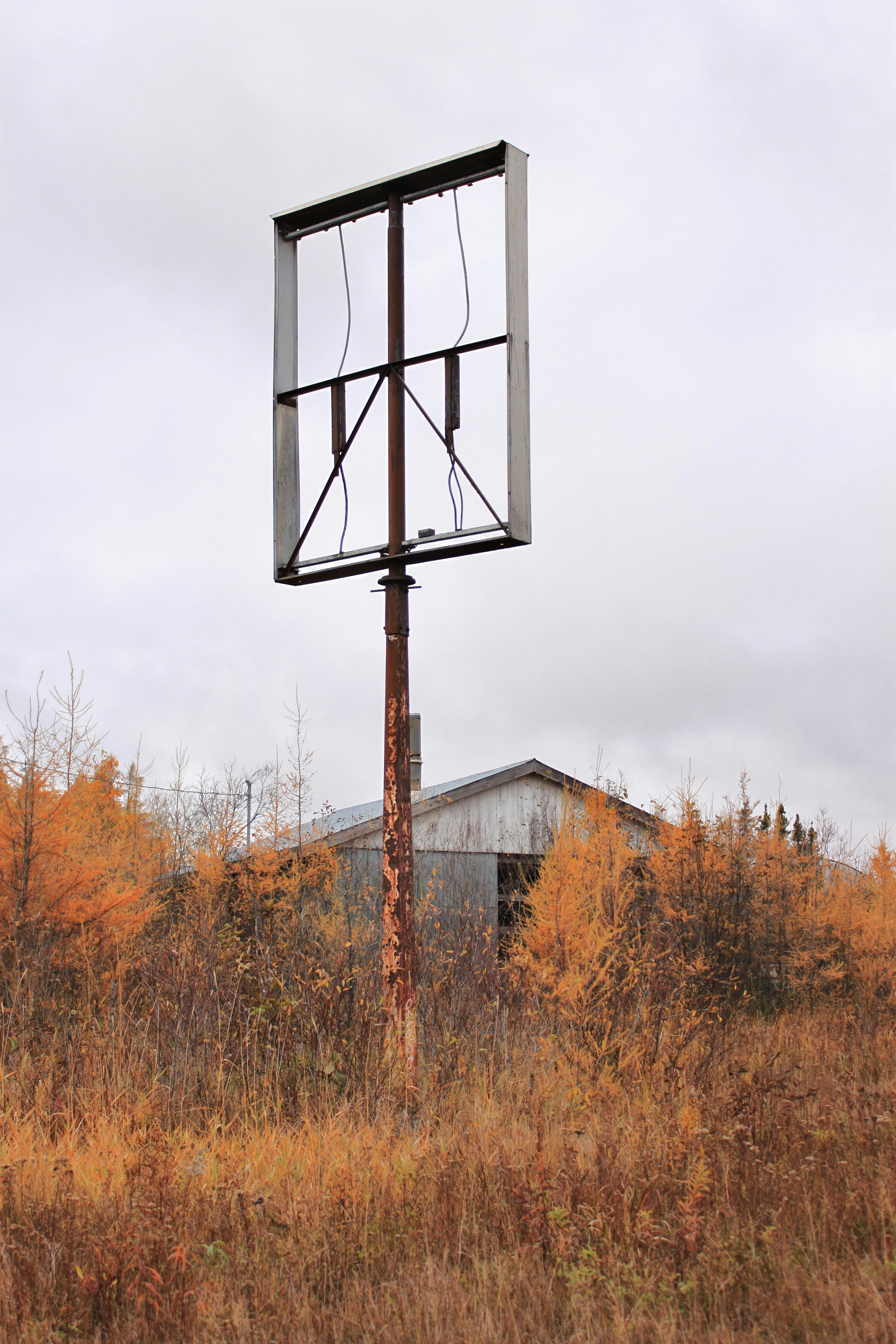 The Silent Frame Above the Field: Rusted Billboard Tower Over a Weathered Barn in Autumn Light