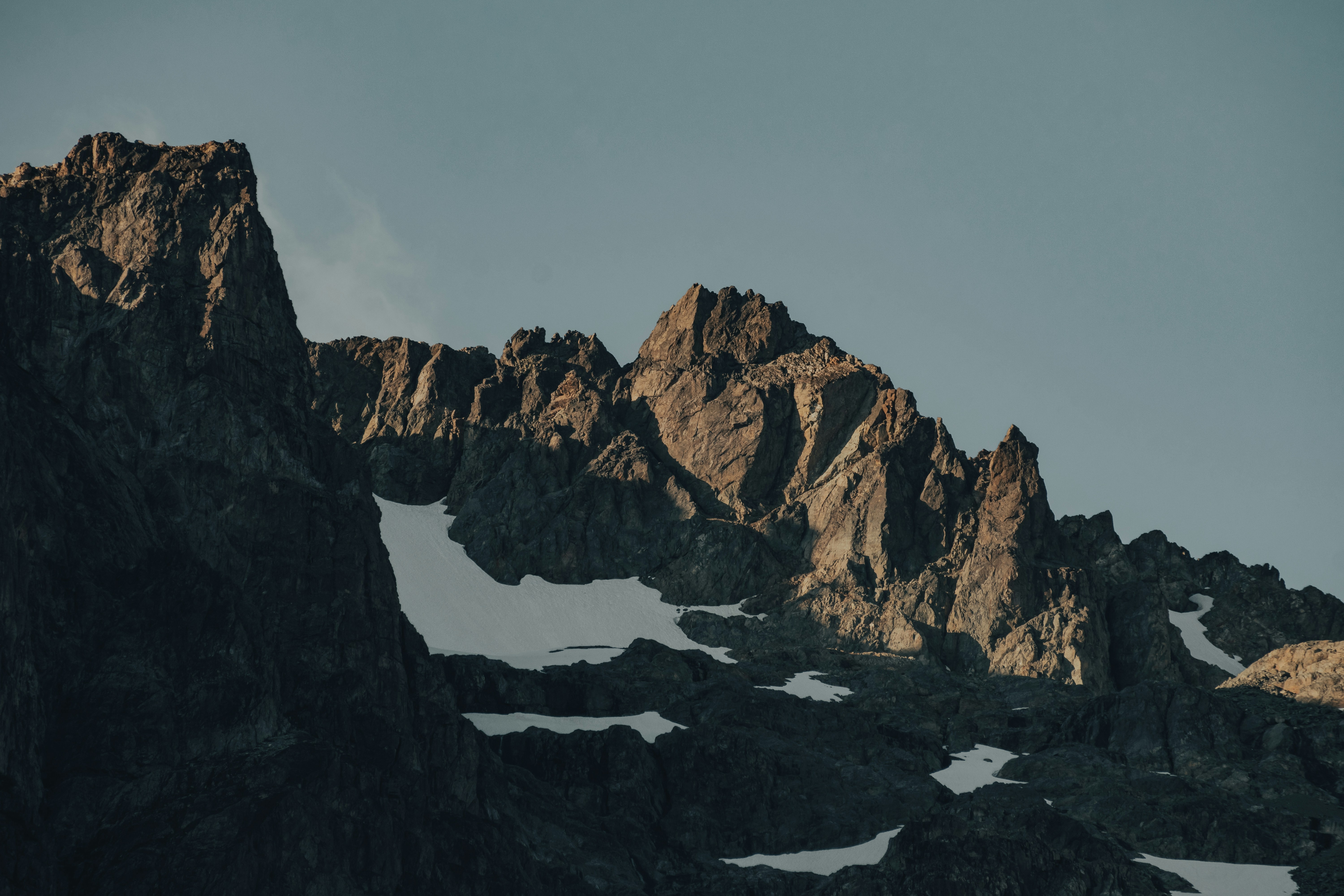 Jagged mountain peaks illuminated by soft light, revealing patches of snow against rugged rock formations.