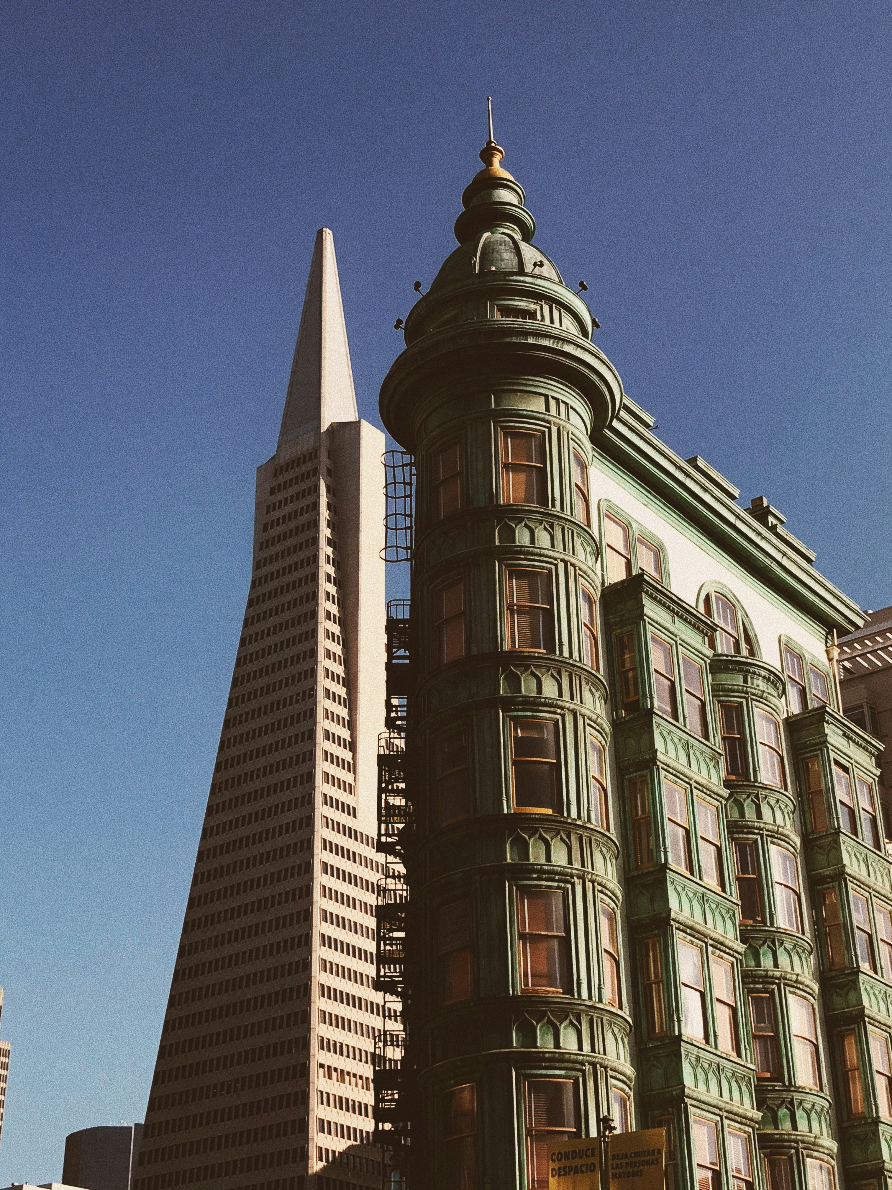 Historic green building standing beside the modern Transamerica Pyramid against a clear blue sky.