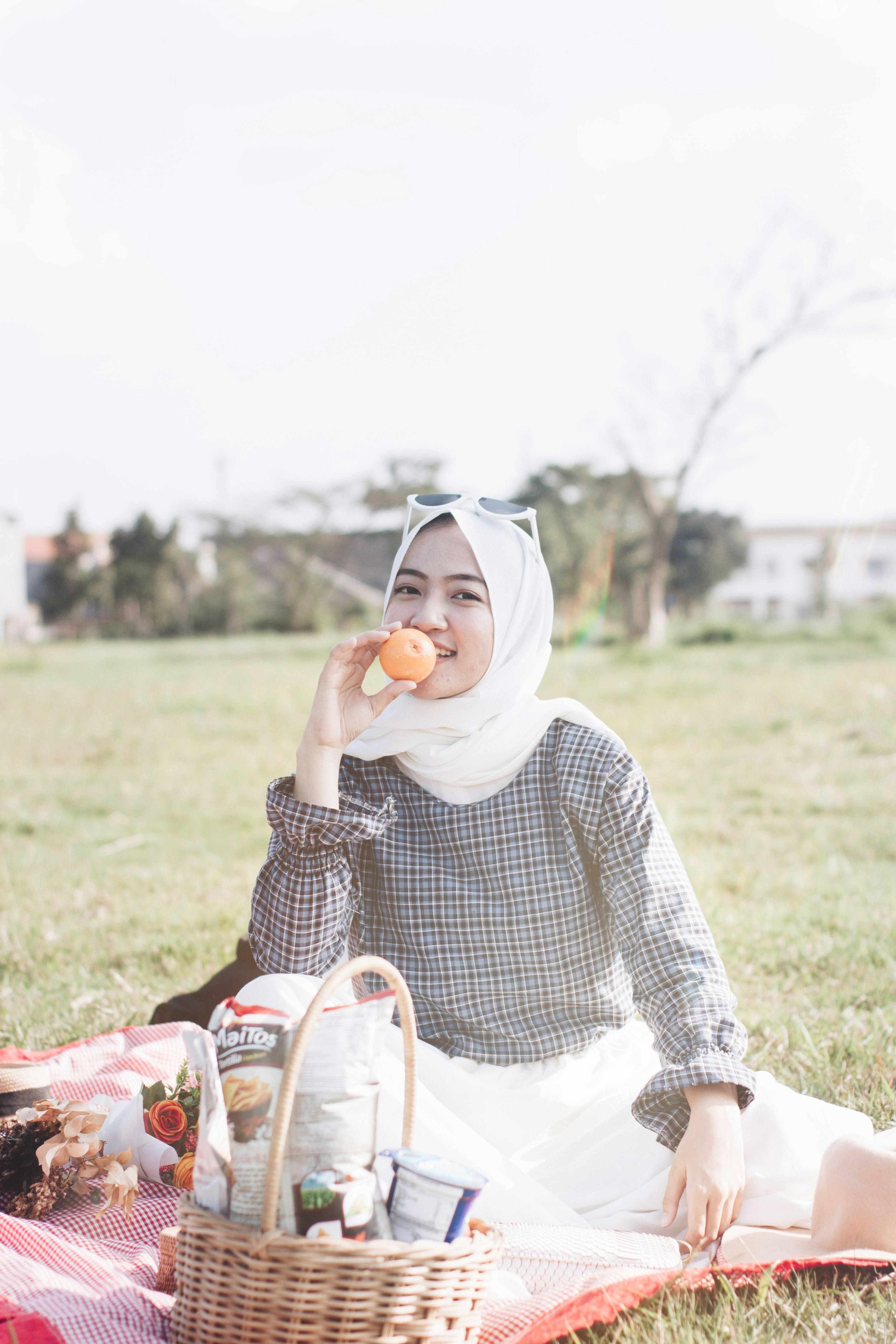 Sunlit Park Picnic: A Hijab-Wrapped Moment with an Orange