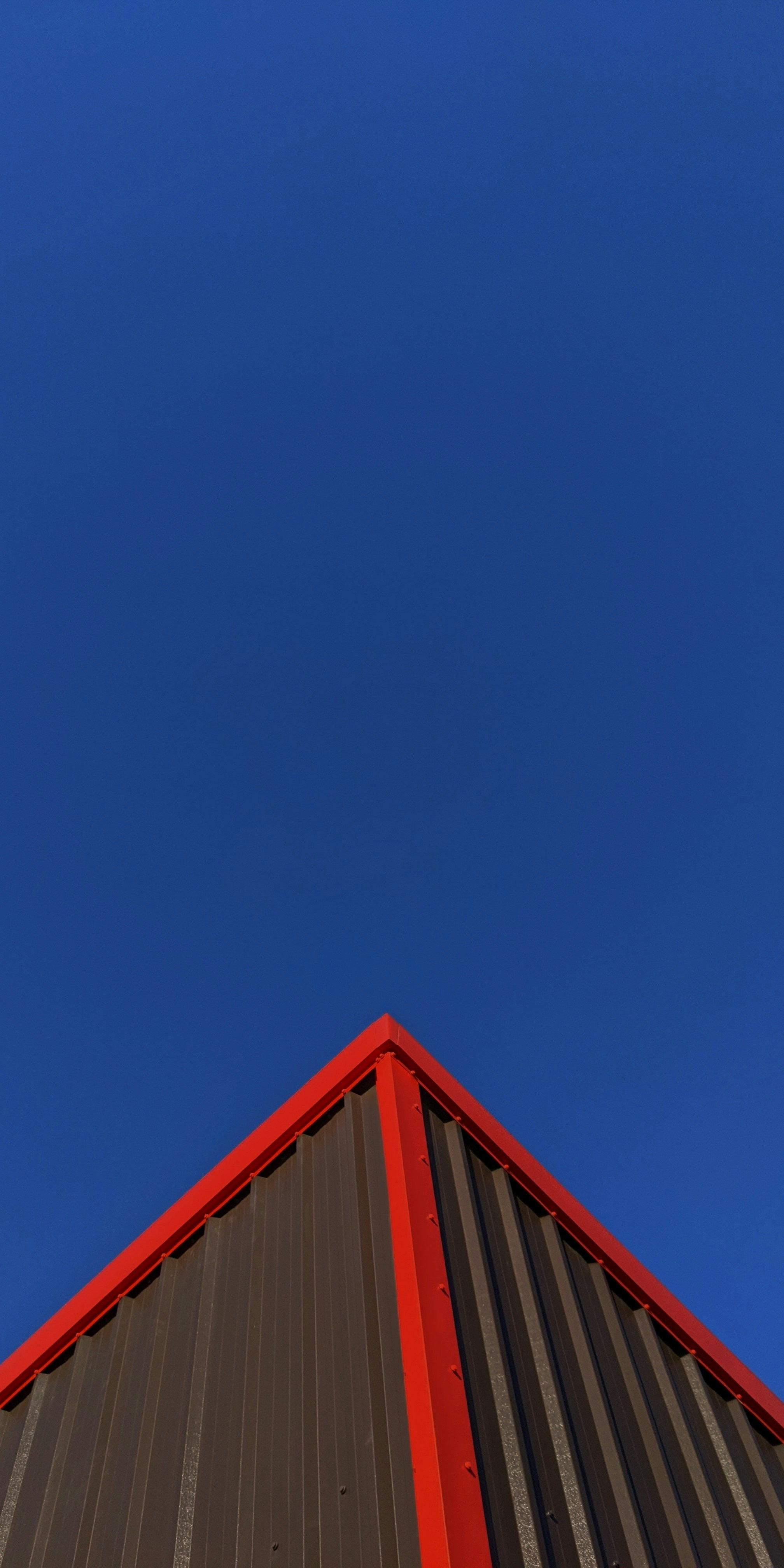 A sharp corner of a building featuring a striking red edge contrasting with a clear blue sky.