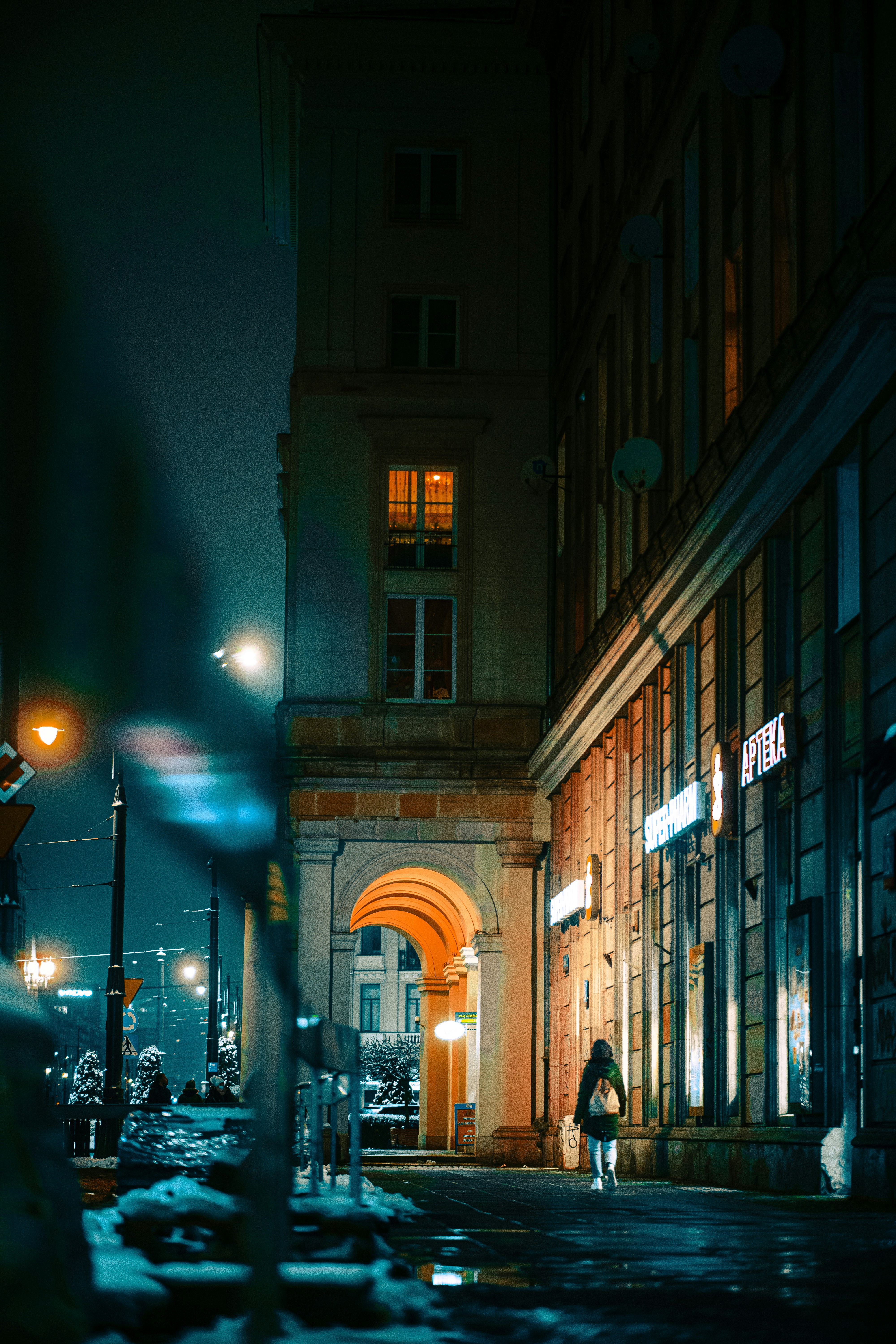 A lone figure walks past illuminated storefronts under a foggy night sky, creating a serene urban atmosphere.