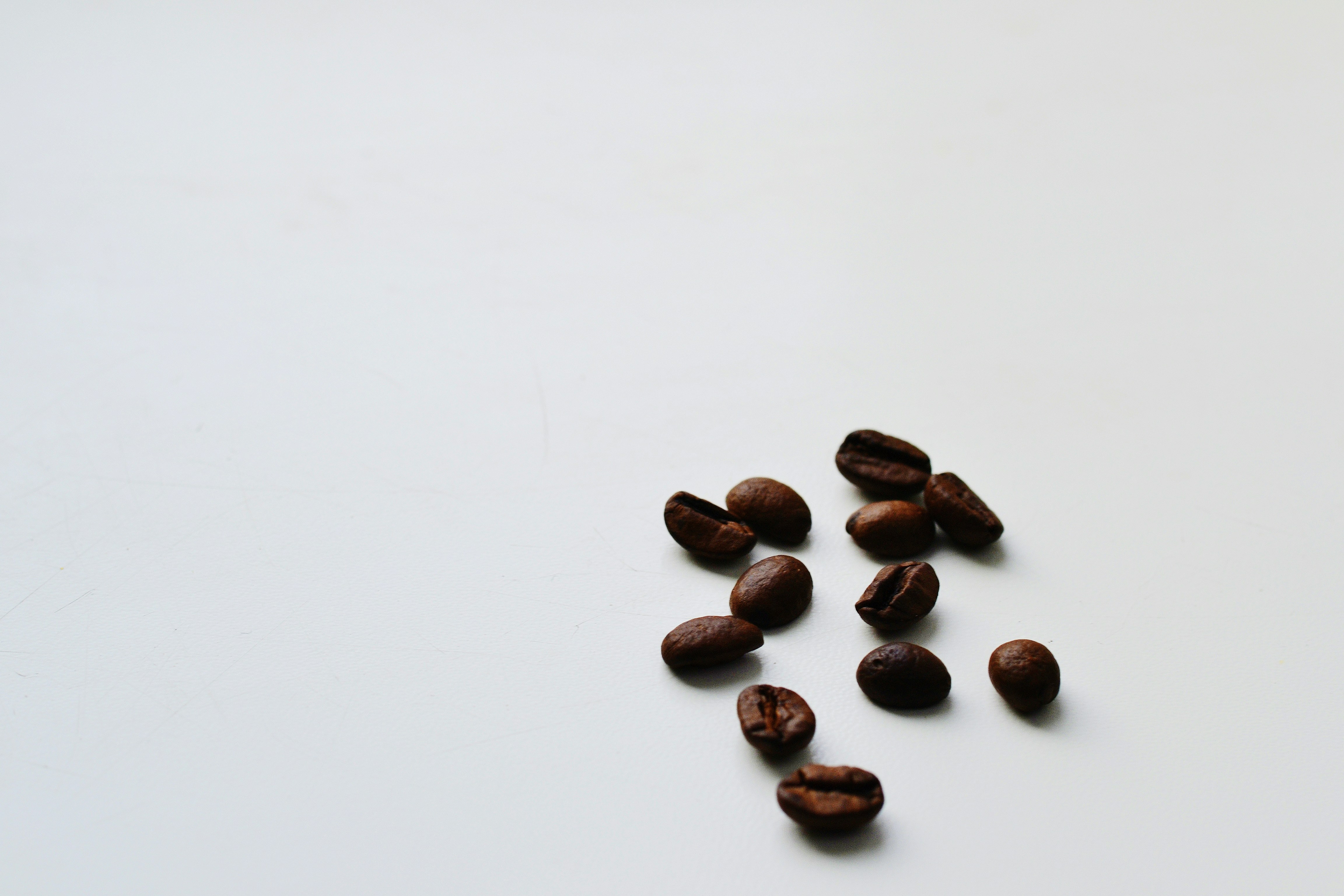 Scattered coffee beans create a minimalist composition on a white surface, emphasizing texture and form.