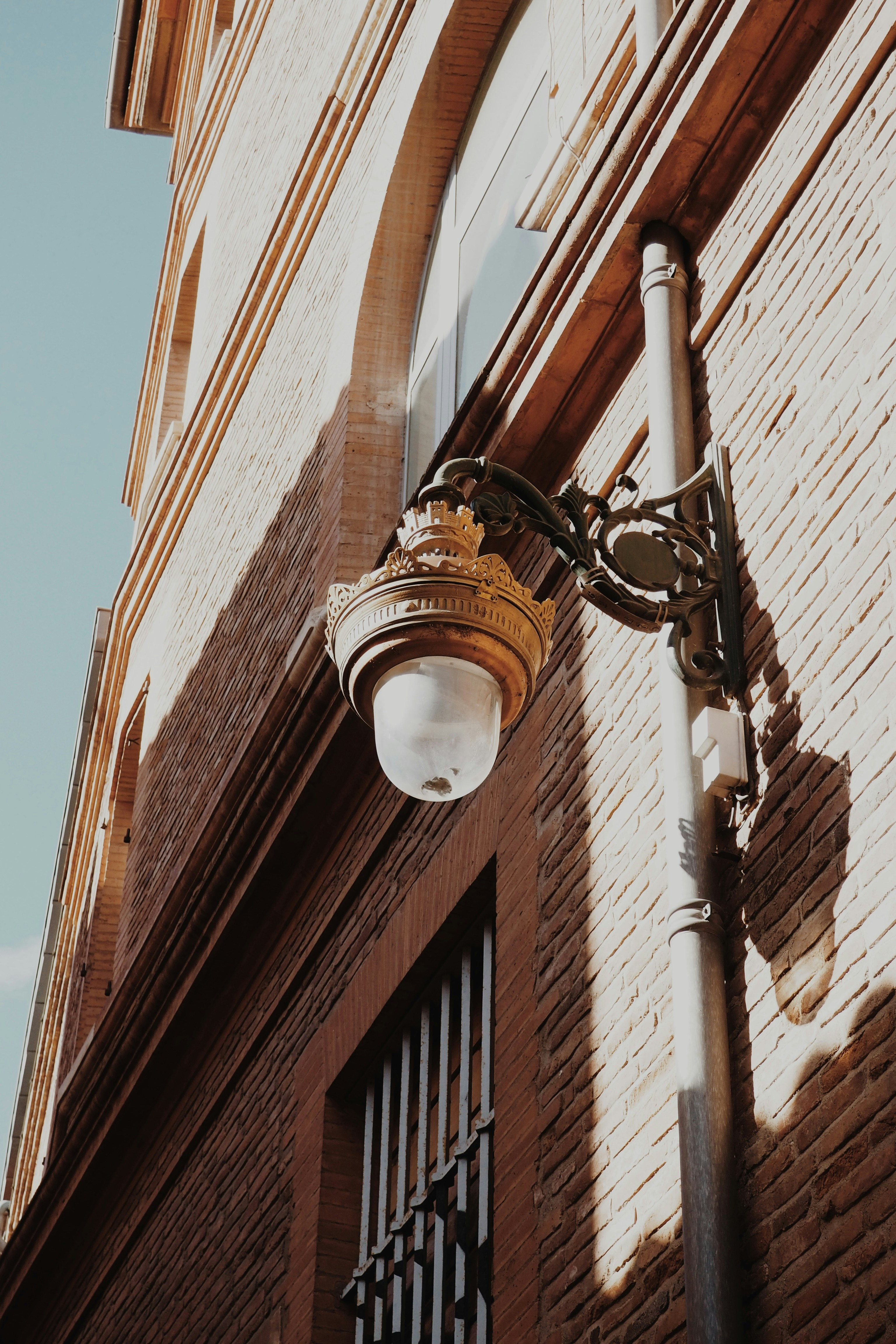 Vintage street lamp affixed to a textured brick wall, casting intricate shadows under a clear blue sky.