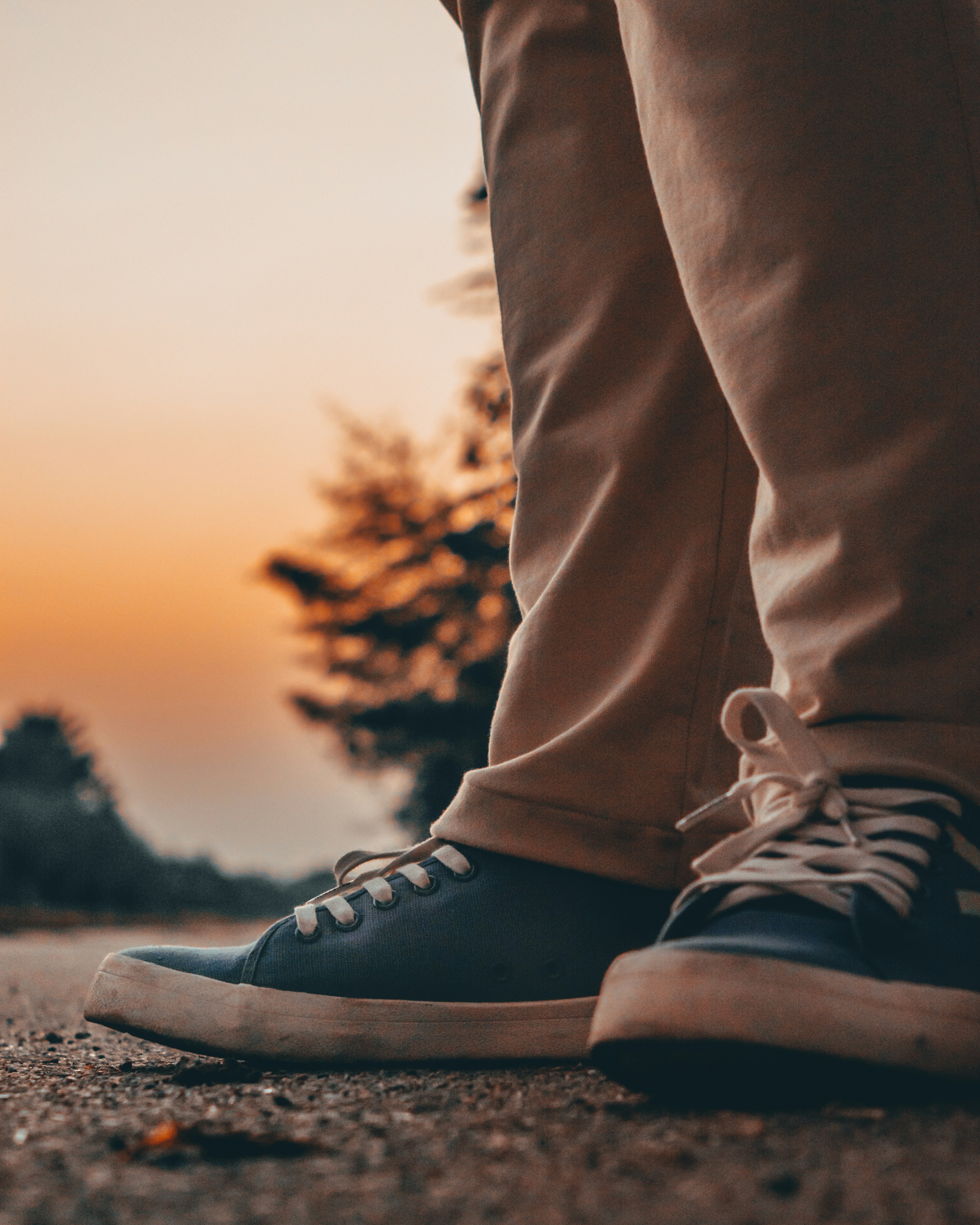 Close-up of sneakers resting on a gravel path with a vibrant sunset in the background.