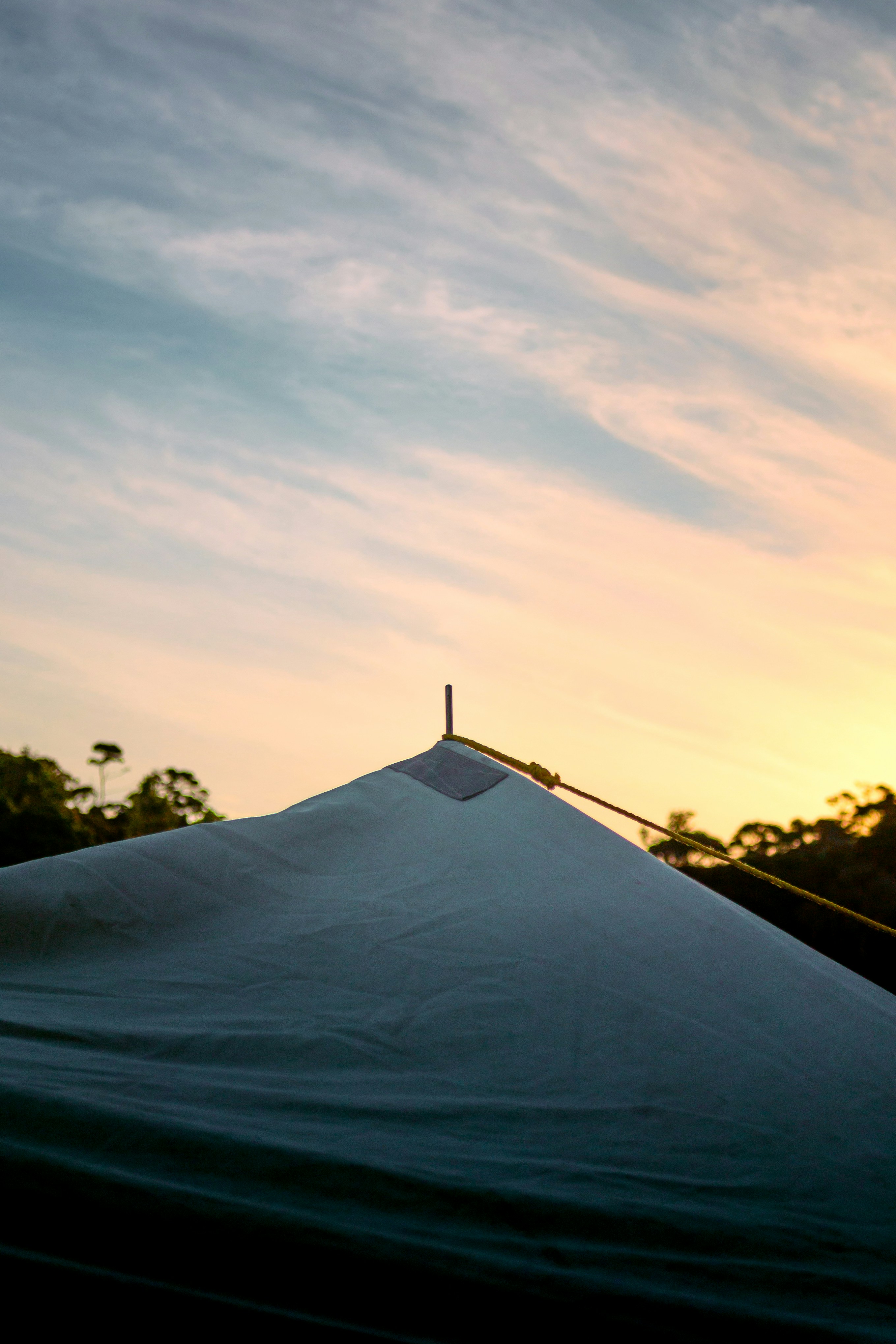 The peak of a tent silhouetted against a vibrant sunset sky, showcasing soft clouds and warm hues.