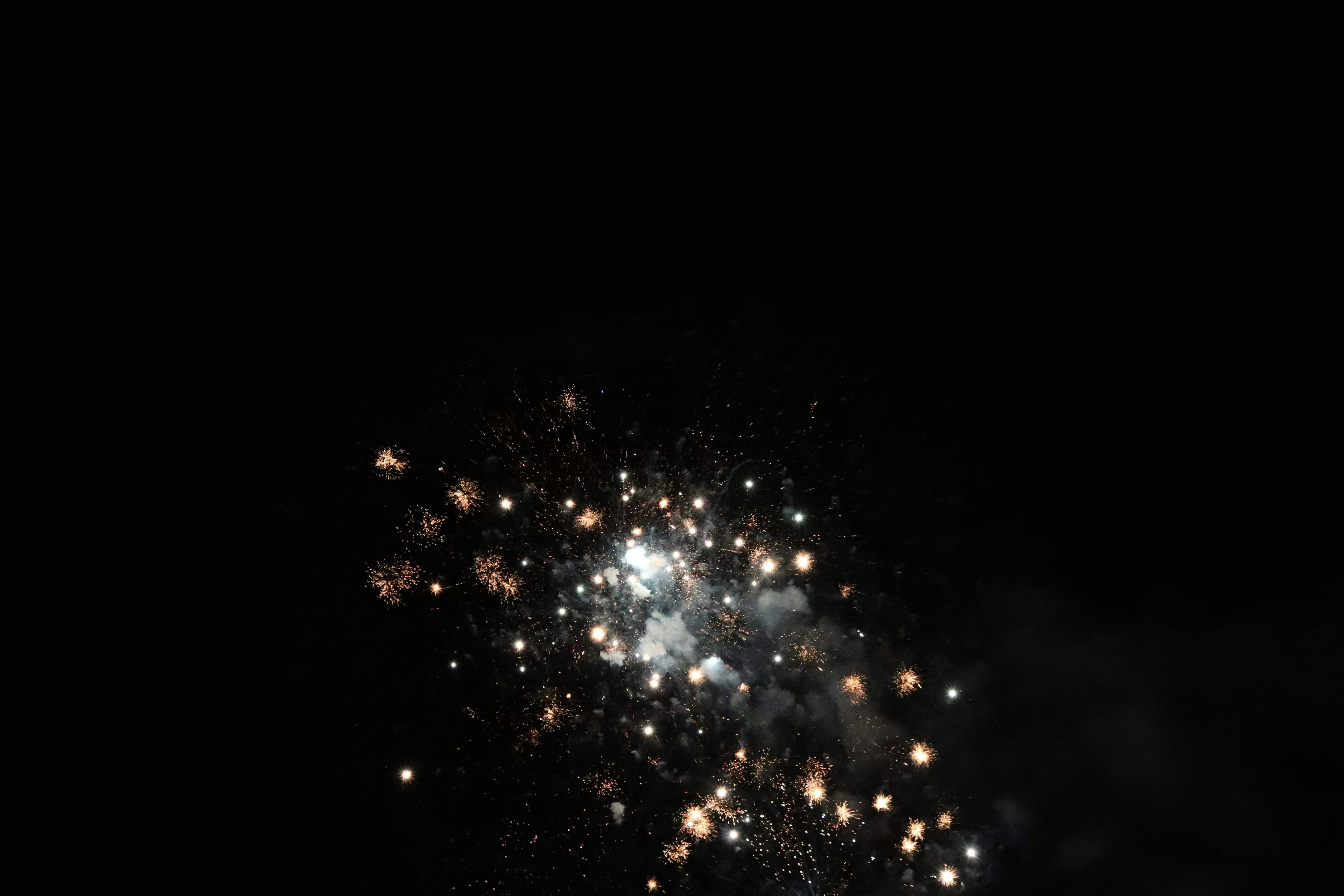 Fireworks explode against a dark night sky, scattering bright sparks and smoke.