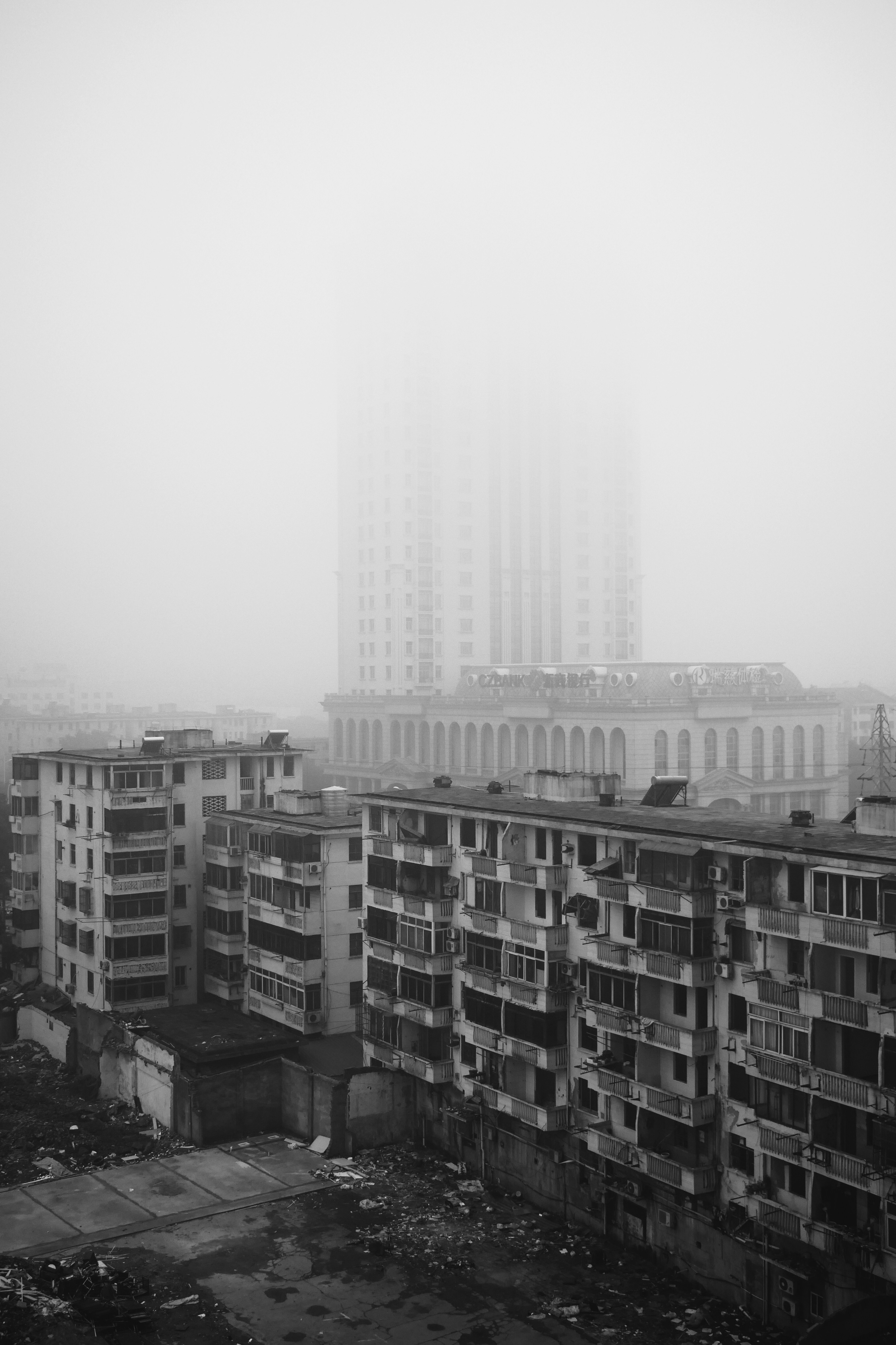 Fog-shrouded cityscape featuring dilapidated buildings in the foreground and a towering structure disappearing into the mist above.