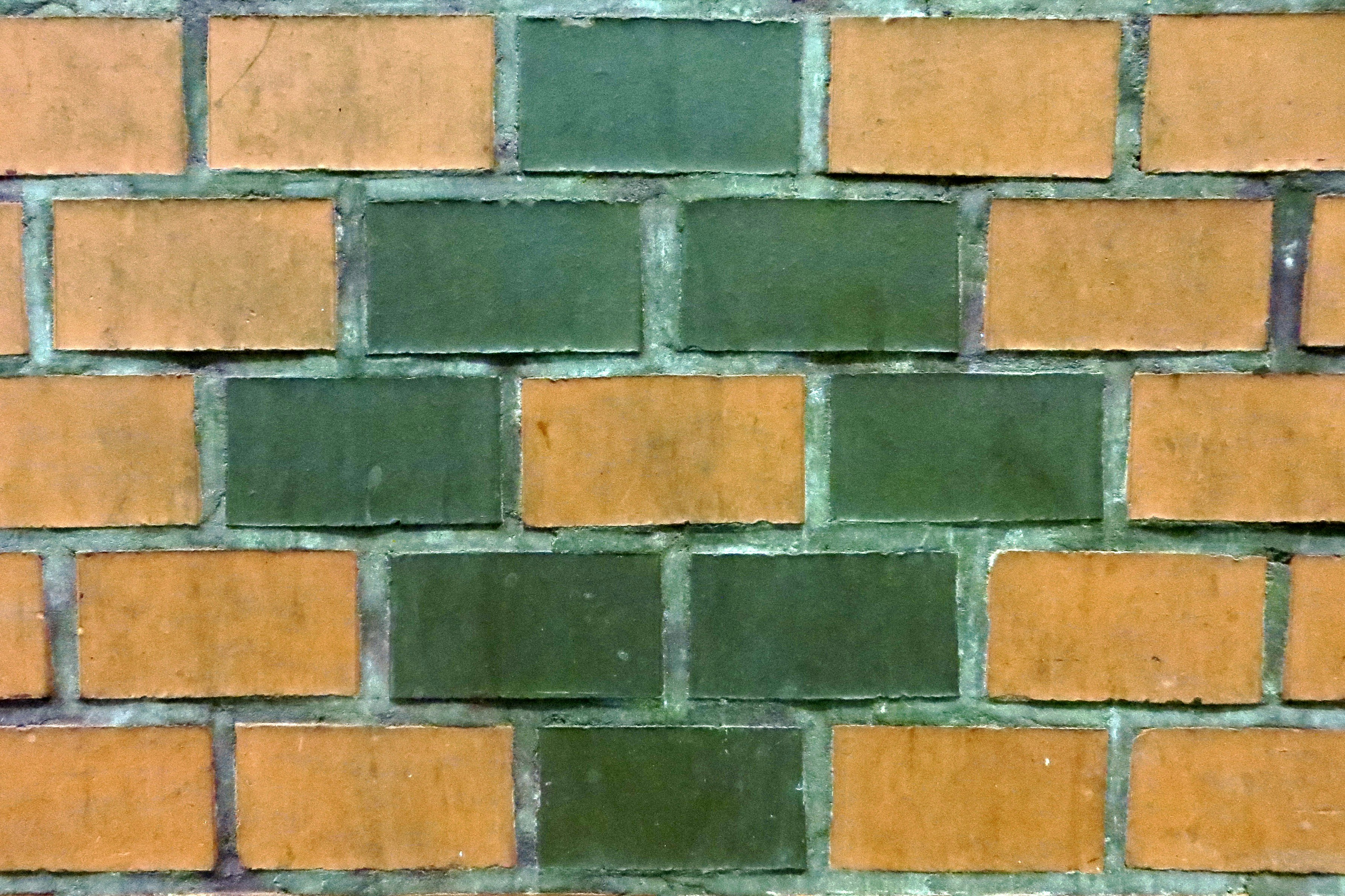 A close-up view of a brick wall featuring alternating green and orange bricks, showcasing a unique pattern and texture.