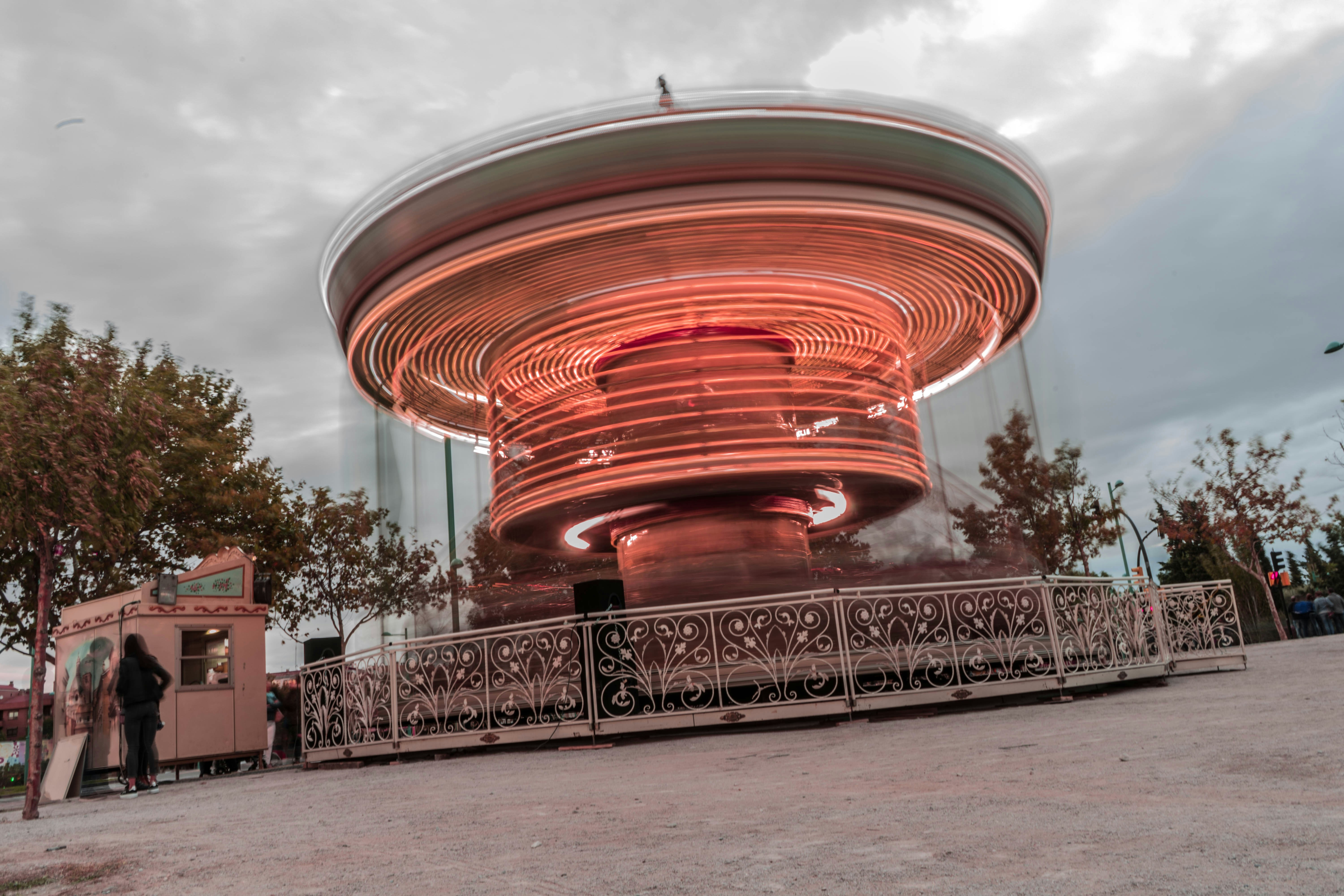 Time-lapse of a carousel spinning under a cloudy sky, capturing trails of light.