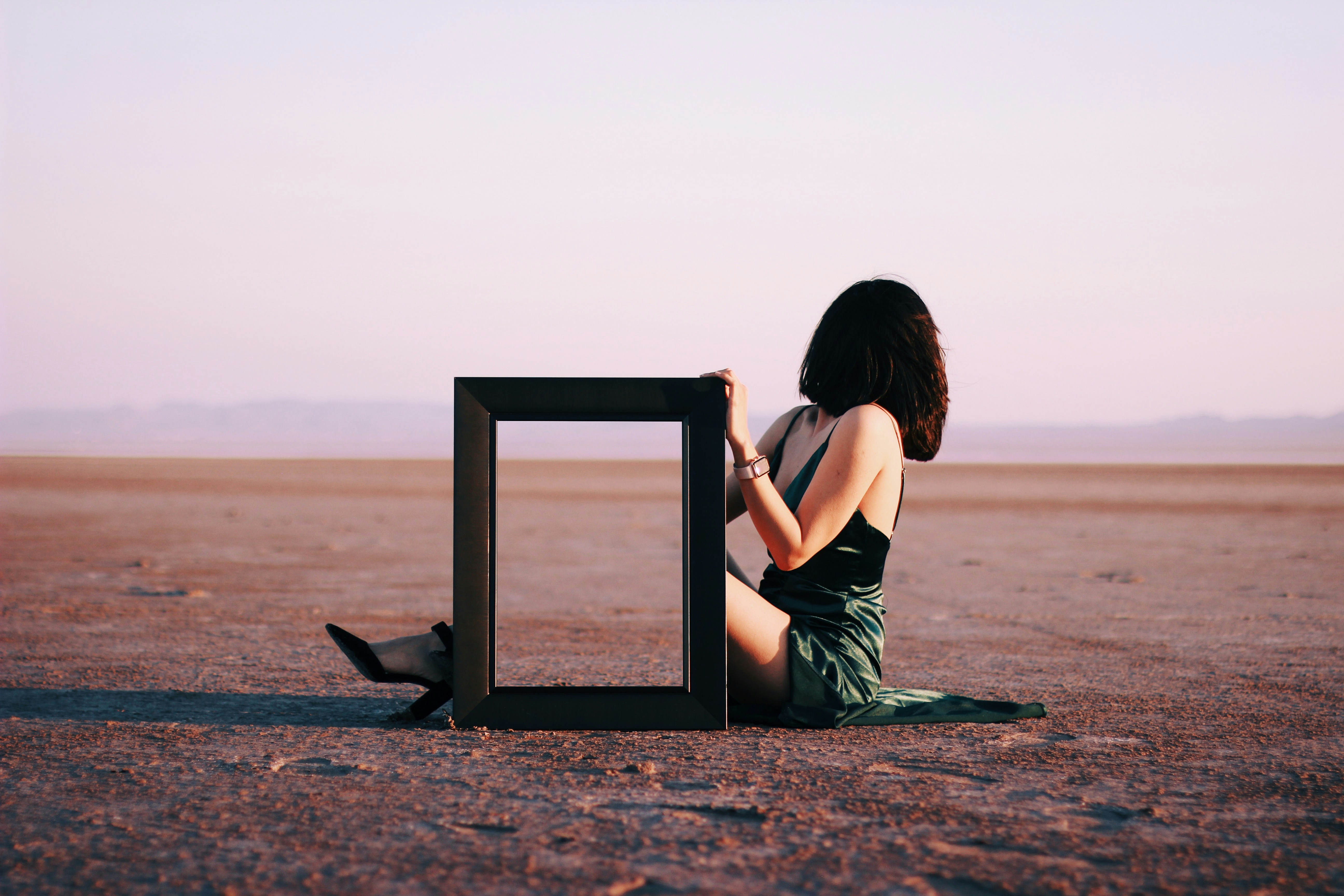 Woman in a black and white striped tank top sitting on expansive brown sand at daytime.