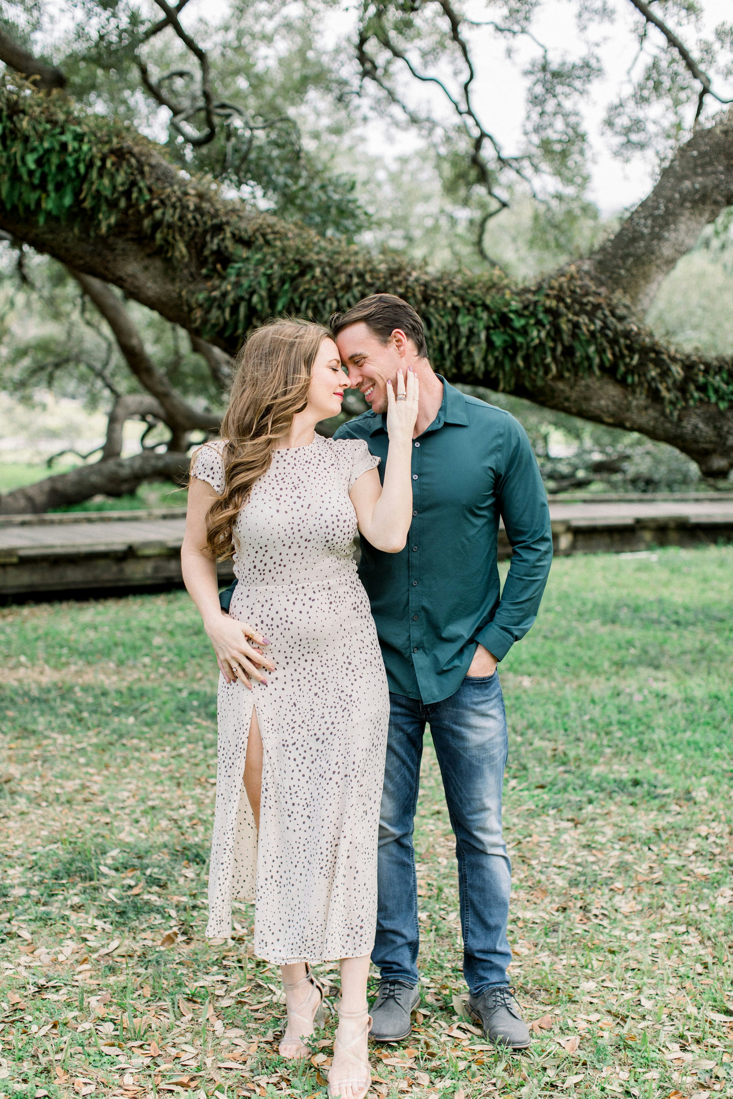 Couple sharing a tender moment beneath a sprawling tree in a serene outdoor setting.