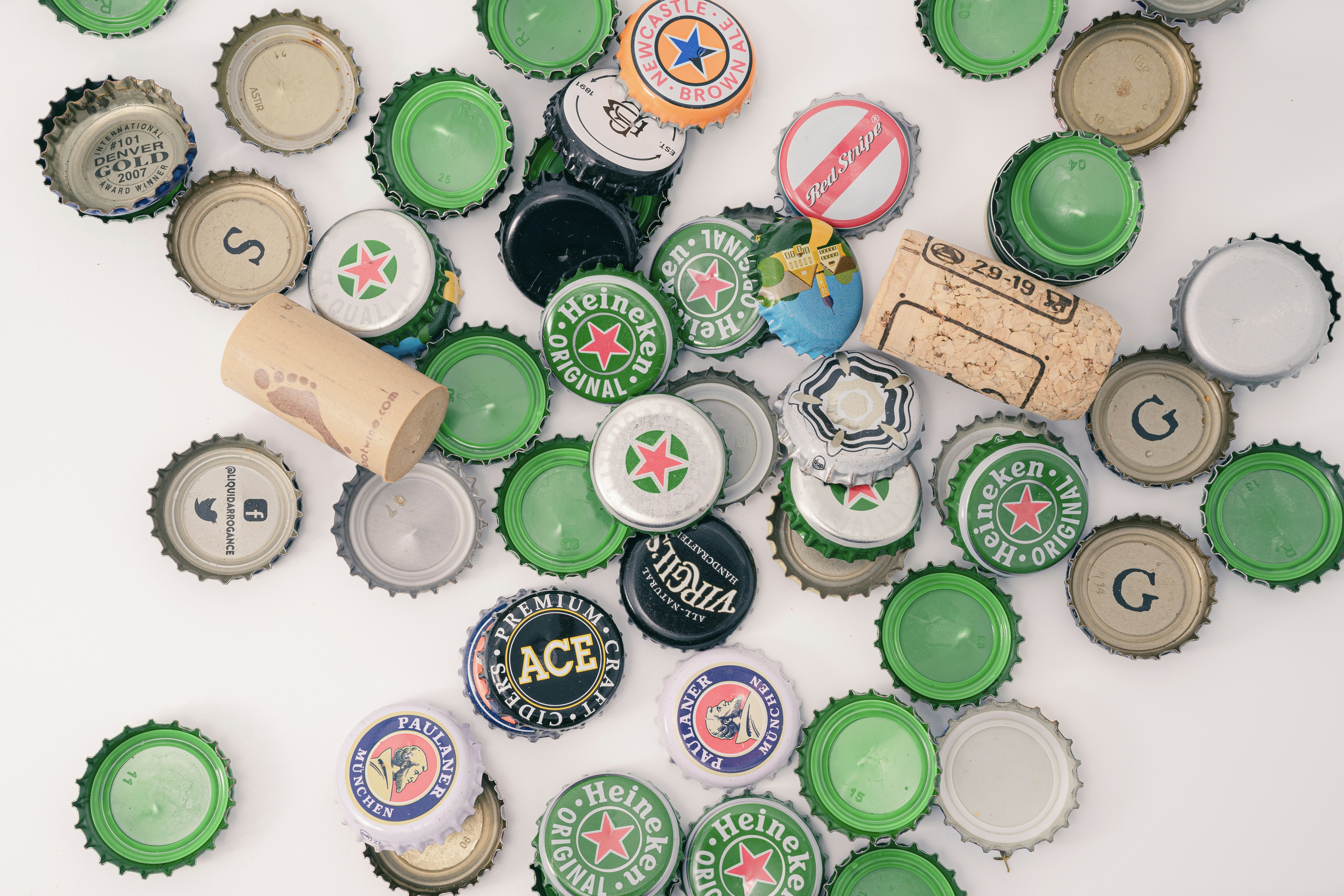 Assorted bottle caps scattered across a white surface, featuring a mix of logos and colors.