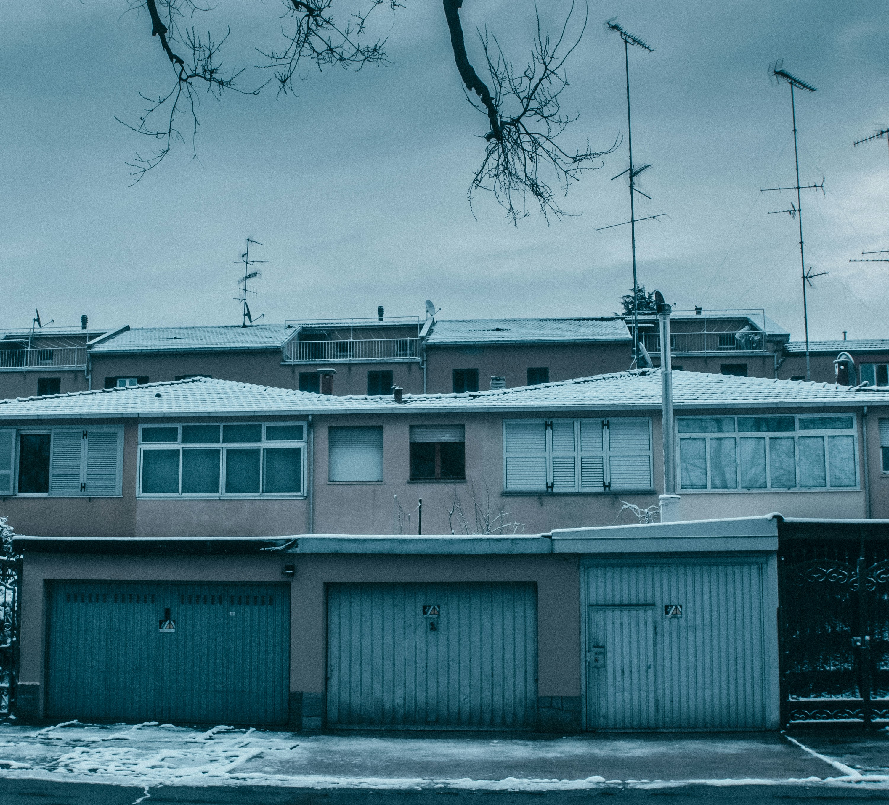 A row of residential garages beneath a cloudy sky, showcasing the starkness of urban life in winter. The muted colors highlight the quiet stillness of the scene.