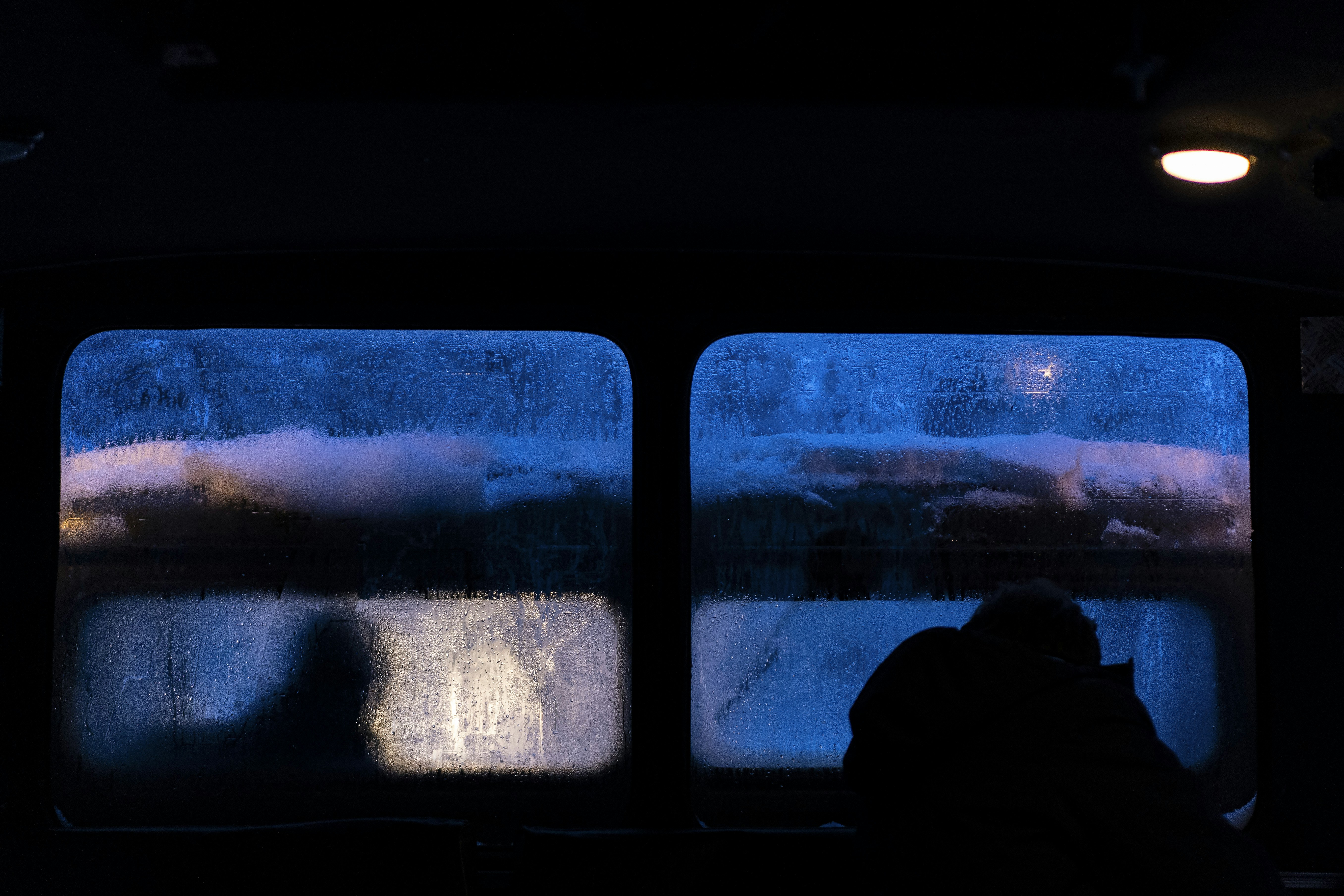 Frosted windows reveal silhouettes of passengers against a wintry backdrop, capturing the essence of a cold journey. The blue tones evoke a serene yet chilling atmosphere.