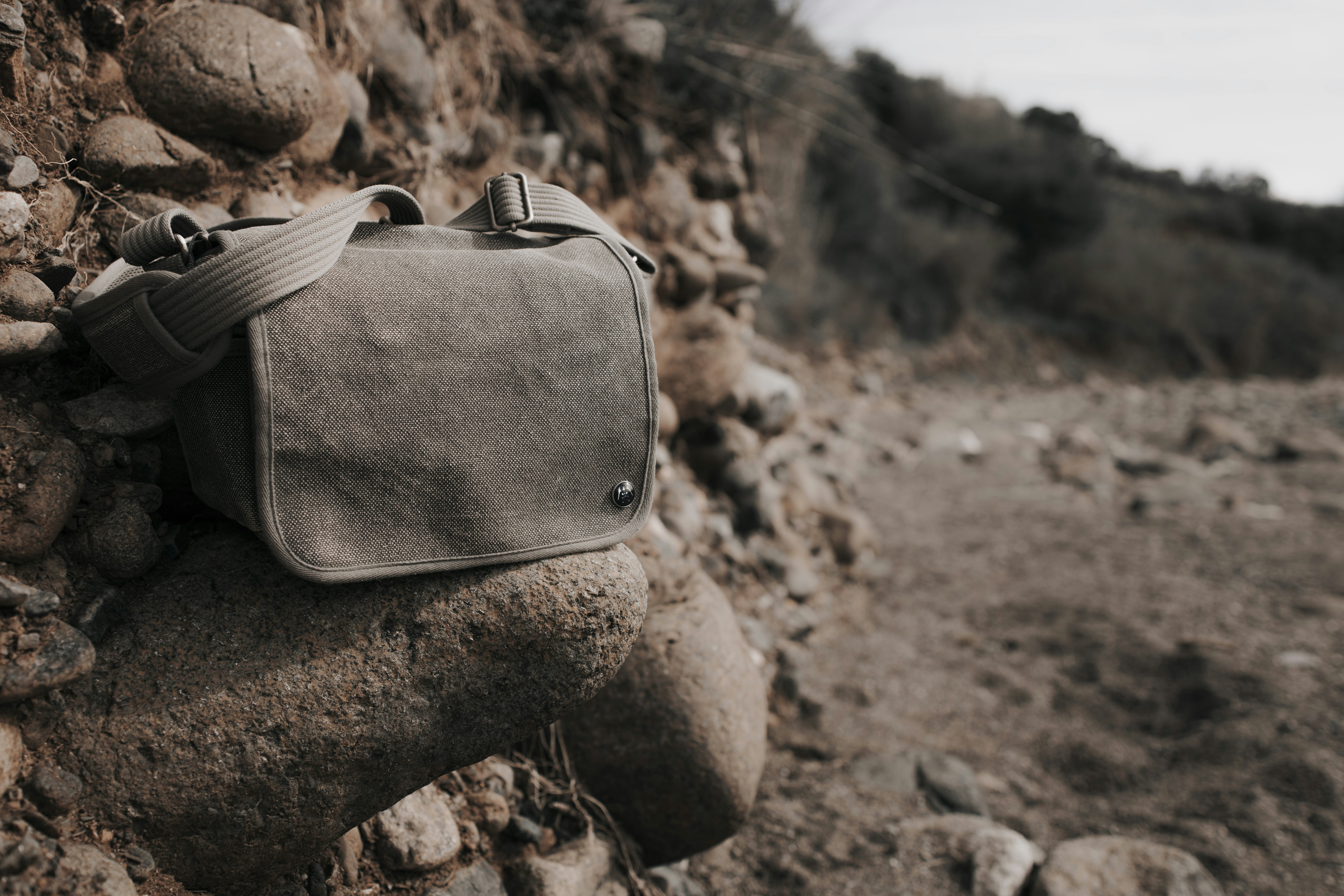 gray leather sling bag on brown rock