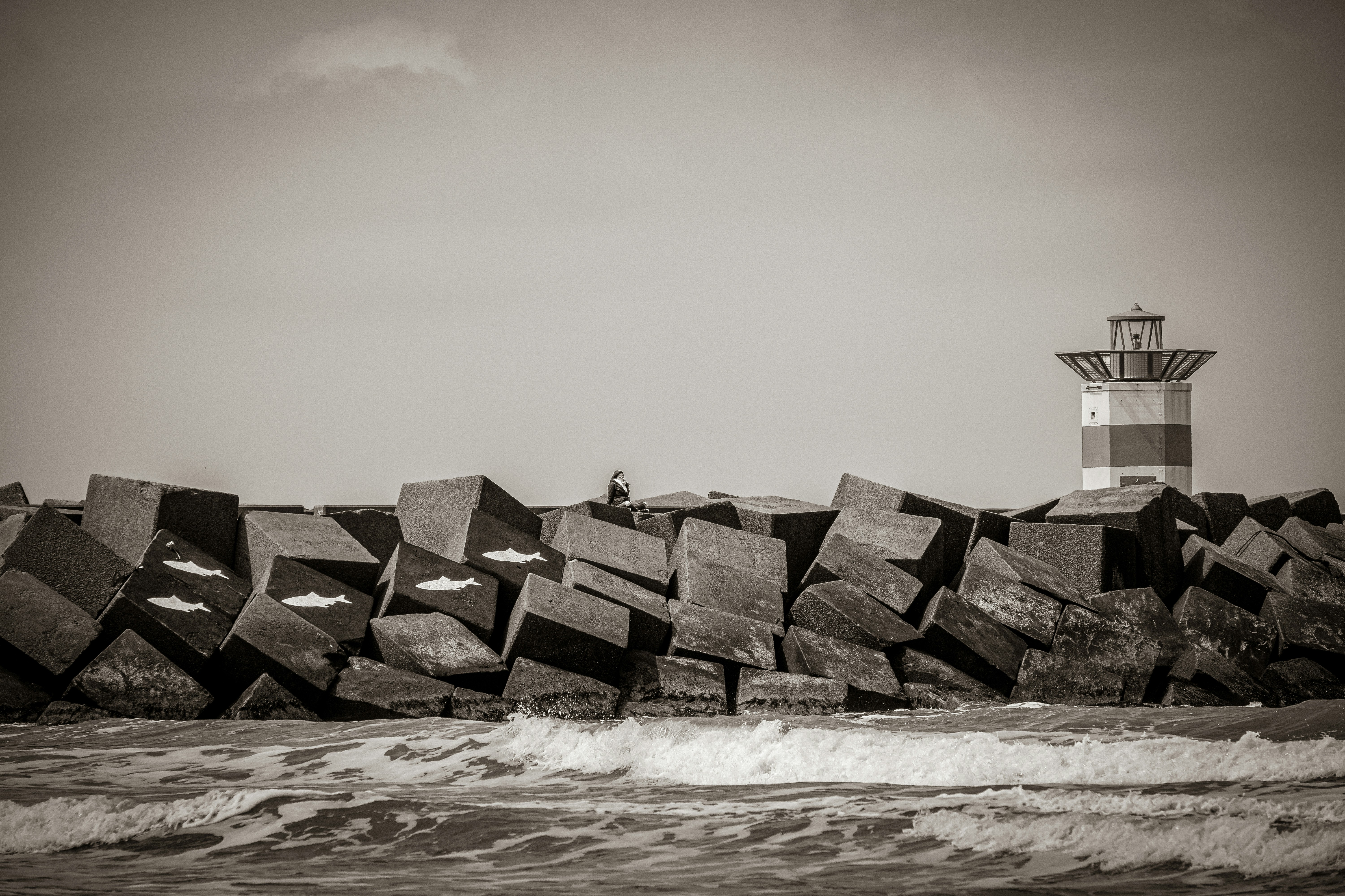 Concrete blocks with painted surfers beside a striped lighthouse on a rocky shore.
