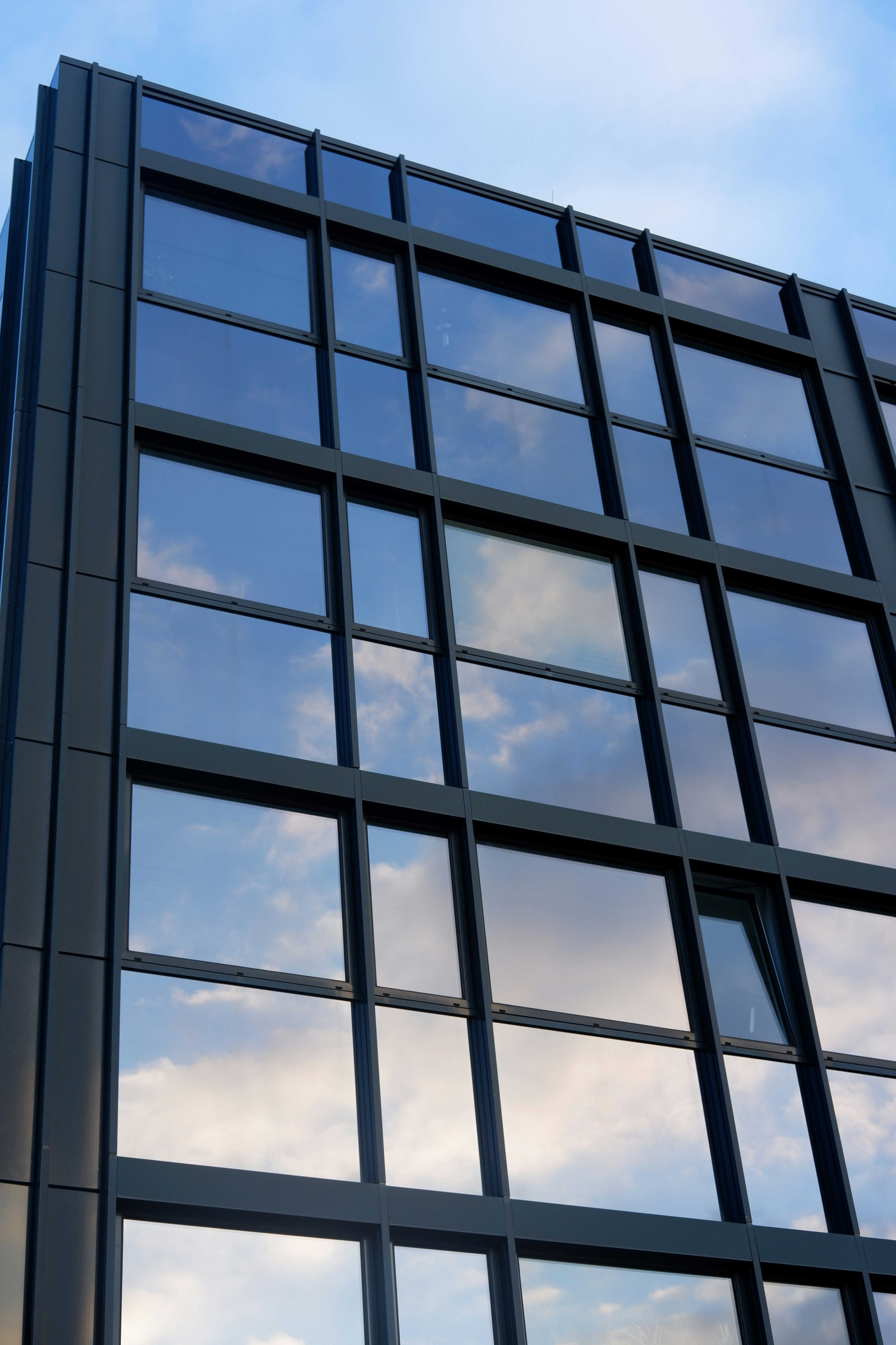 Glass building facade reflecting a serene blue sky with scattered clouds.