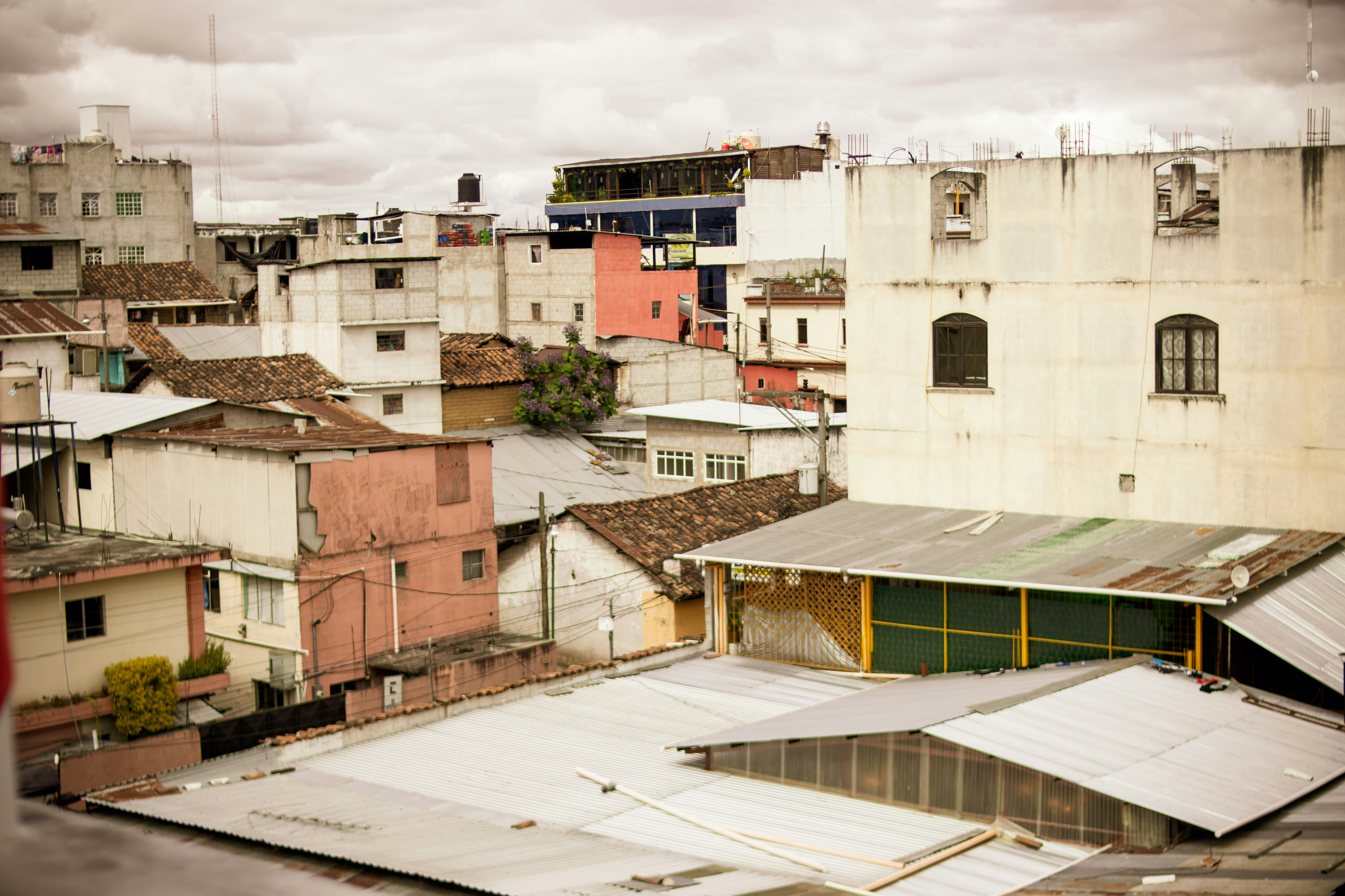 Eclectic mix of rooftops and buildings in a densely packed urban landscape under a cloudy sky.