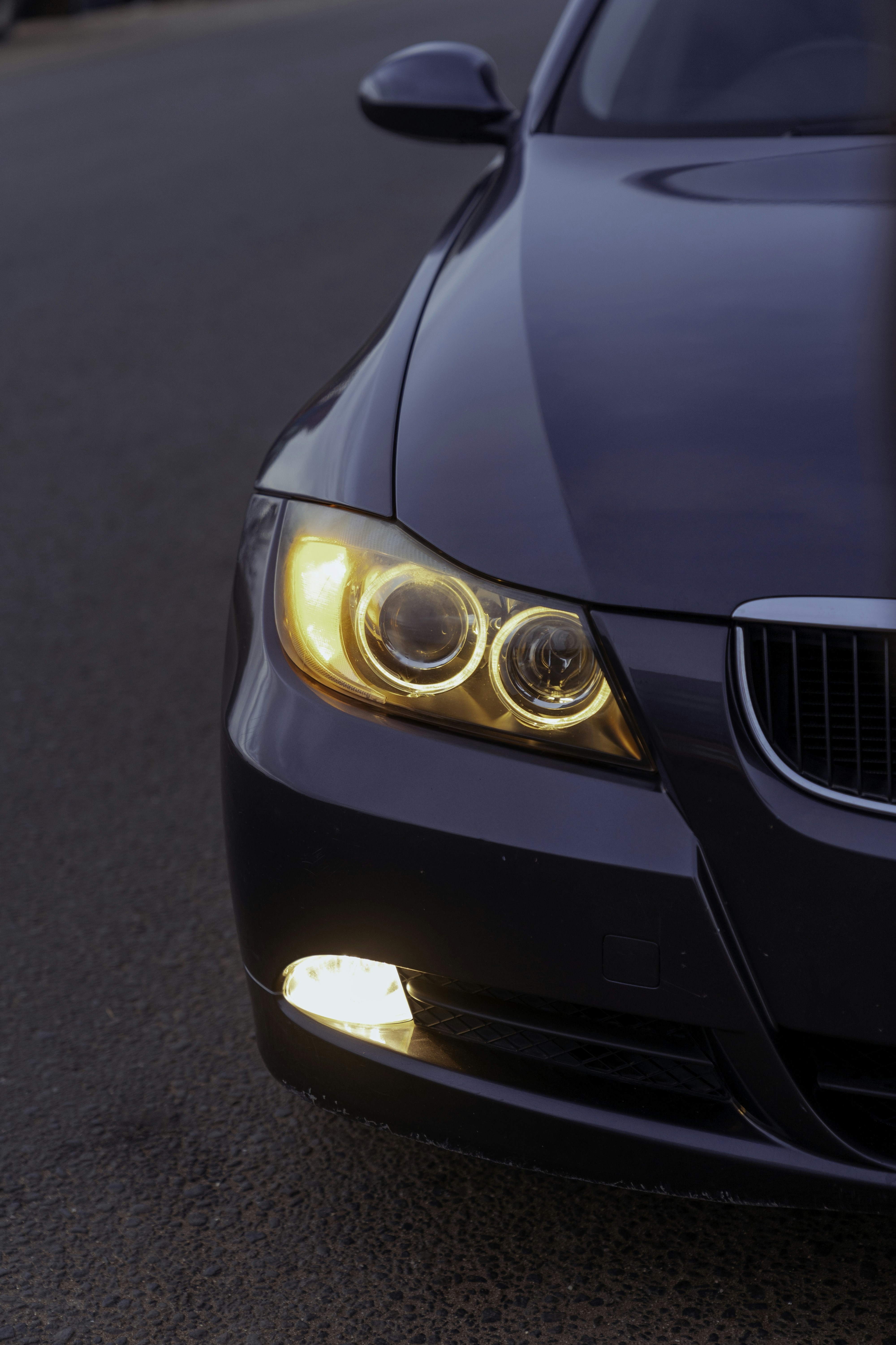 Close-up of a car's illuminated front headlights against a dimly lit street.
