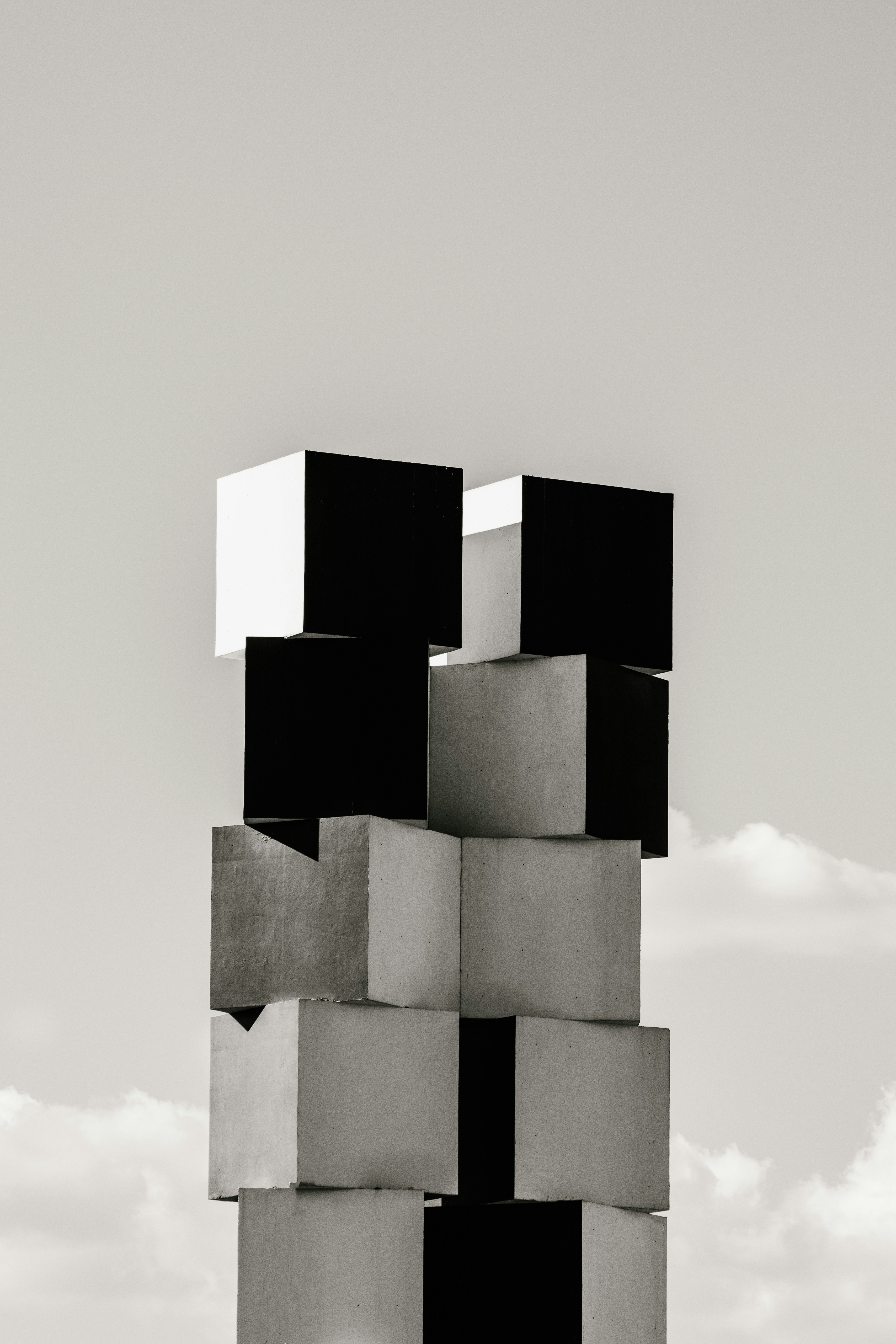 A striking arrangement of stacked cubes in contrasting black and white, set against a soft sky. The architectural structure emphasizes geometric forms and shadows.