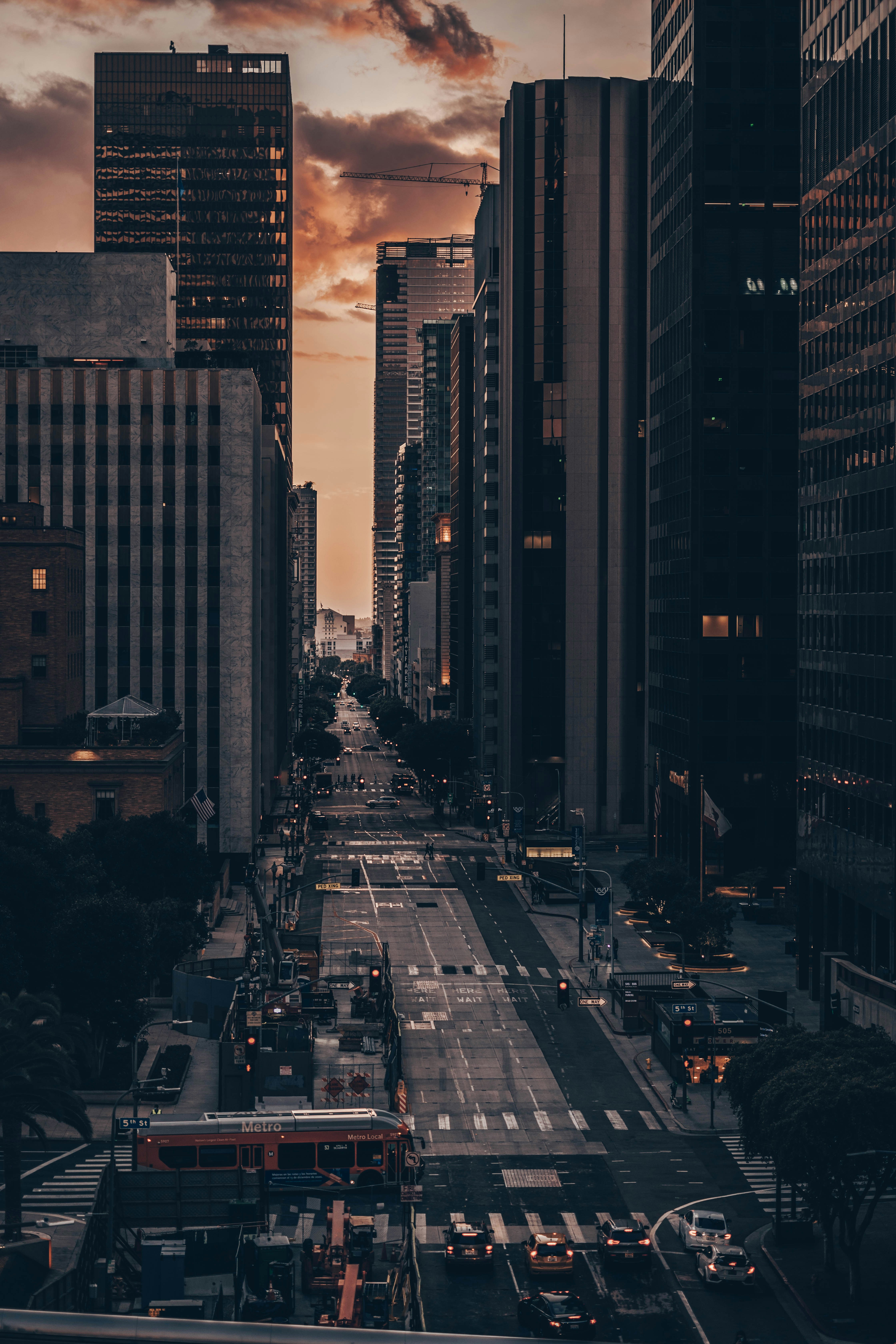 A bustling city street at twilight, framed by towering skyscrapers and a dramatic sky. The scene captures the vibrant energy of urban life as vehicles navigate the thoroughfare.