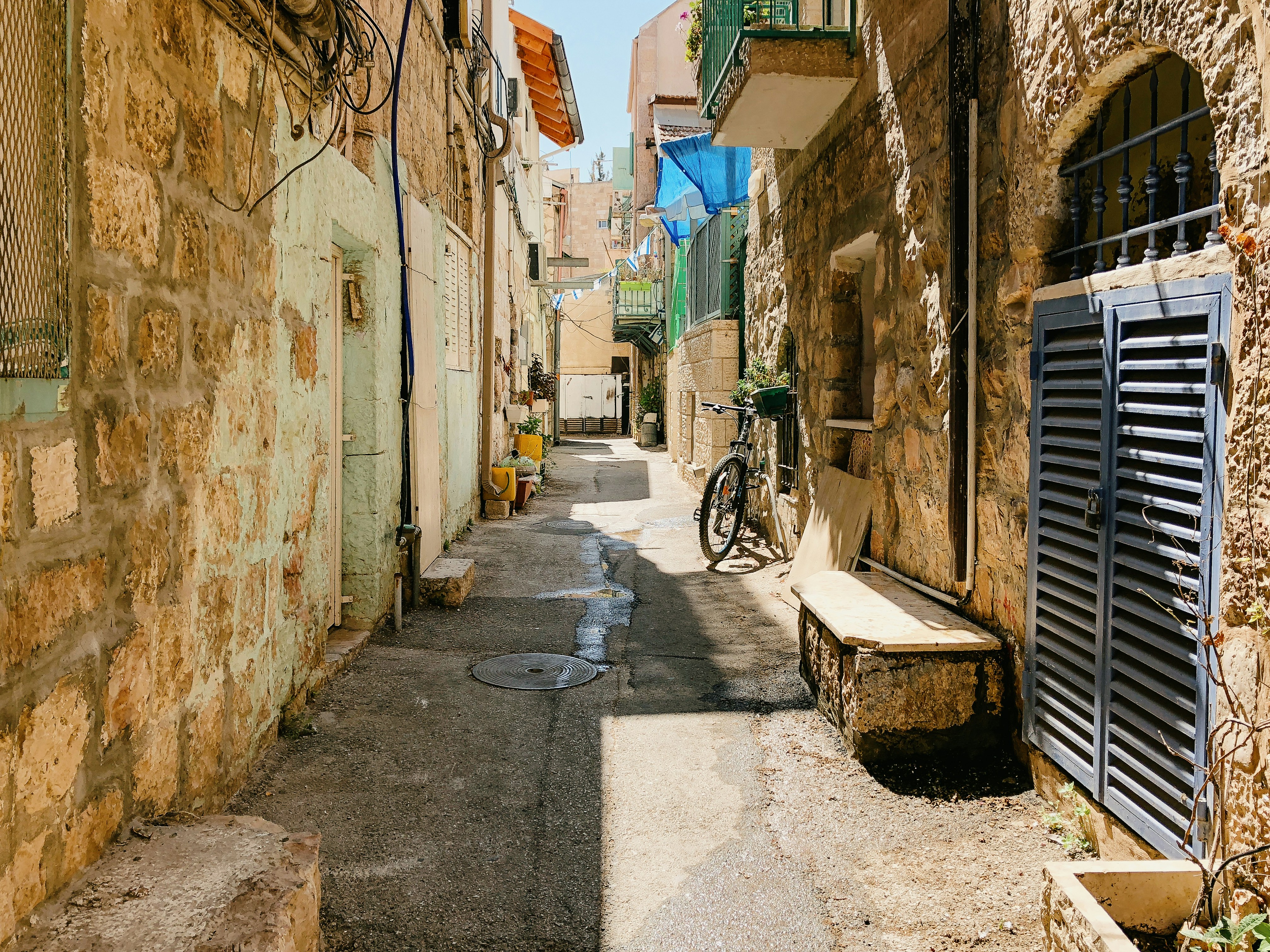 Narrow alley with a black bicycle leaning against a stone wall, bathed in warm sunlight.
