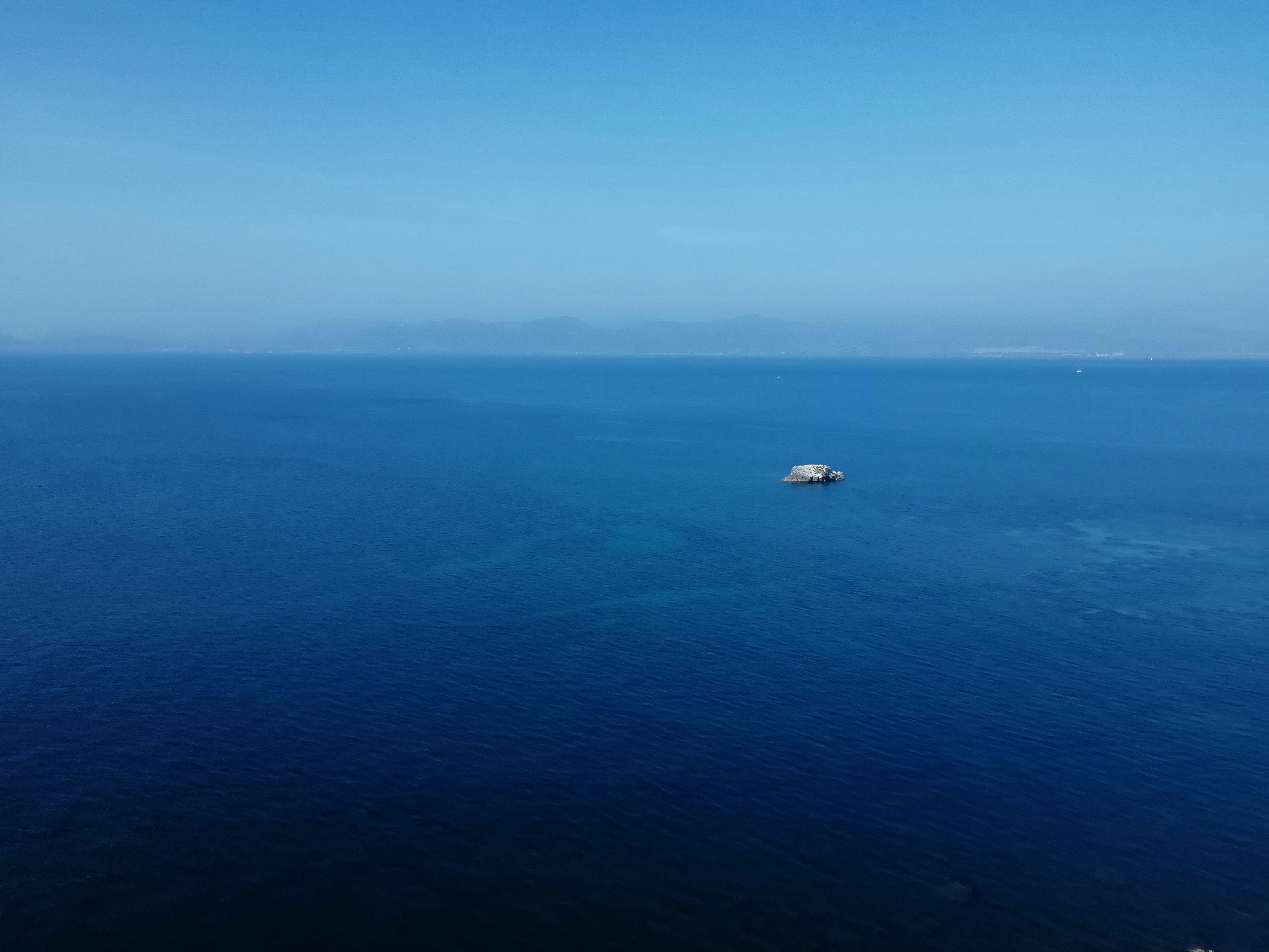A solitary structure rests on the serene blue waters, surrounded by distant hills under a clear sky.