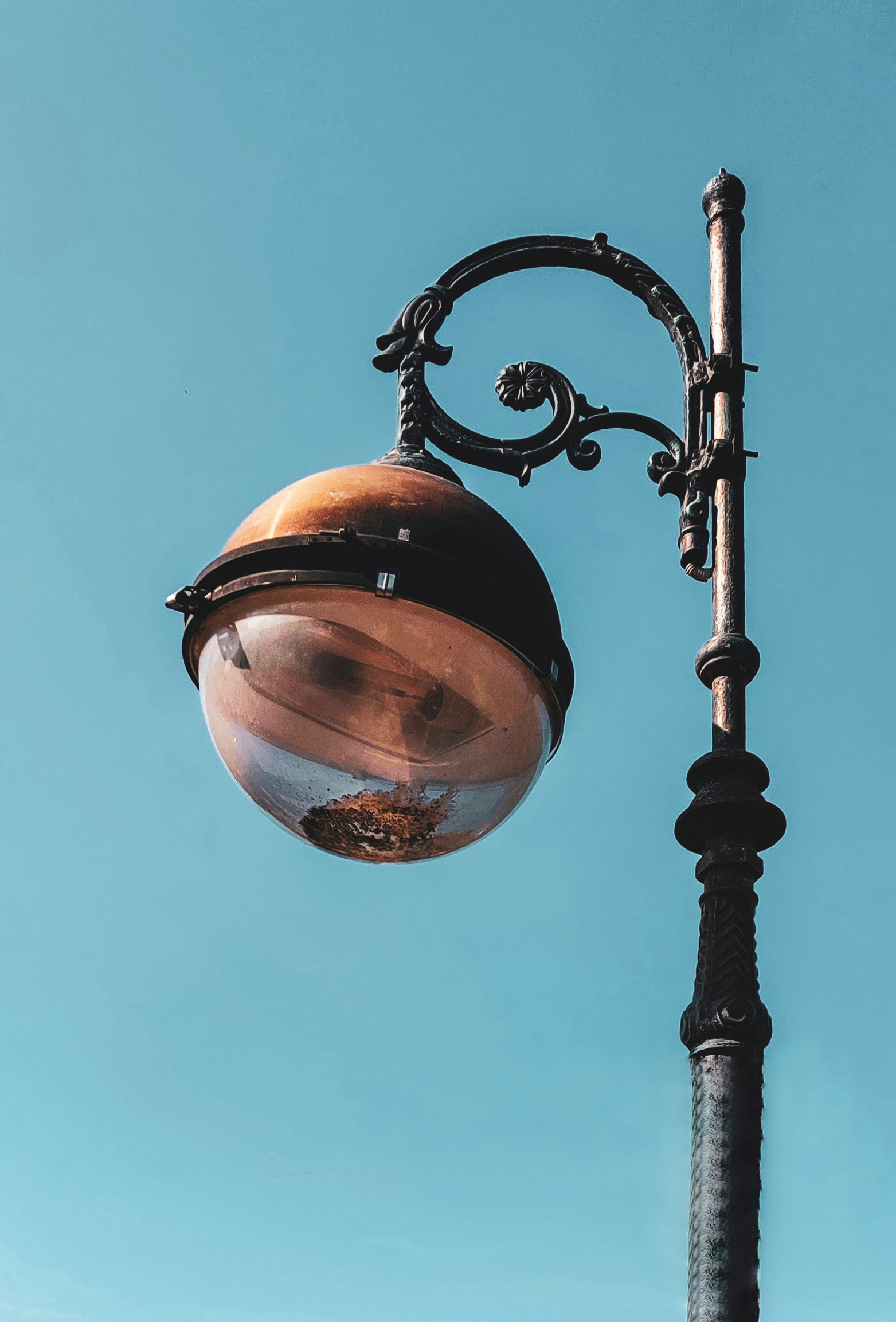 Ornate vintage streetlamp with a spherical glass lantern set against a bright blue sky.