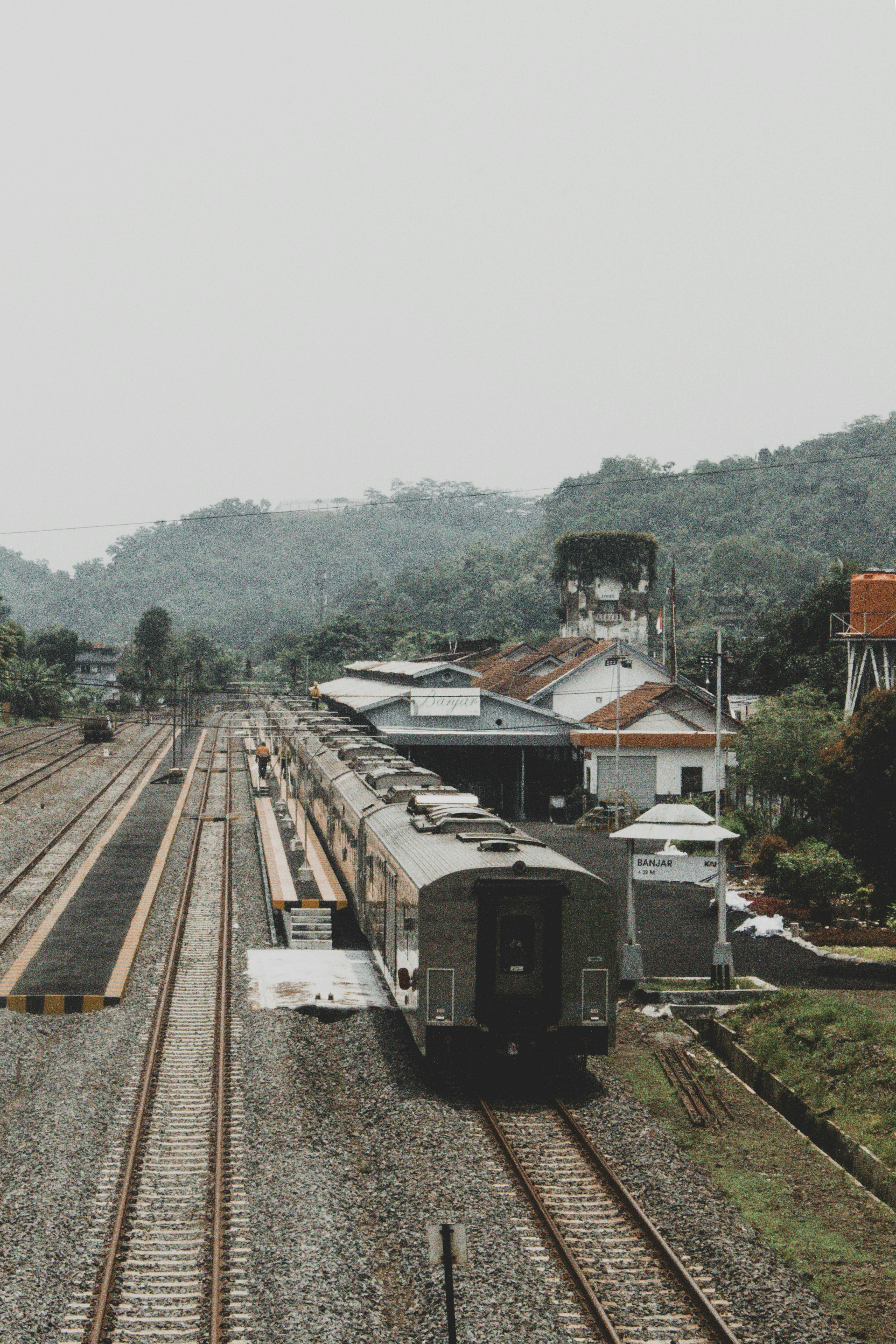 Train at a rural station with lush hills in the background on a cloudy day.