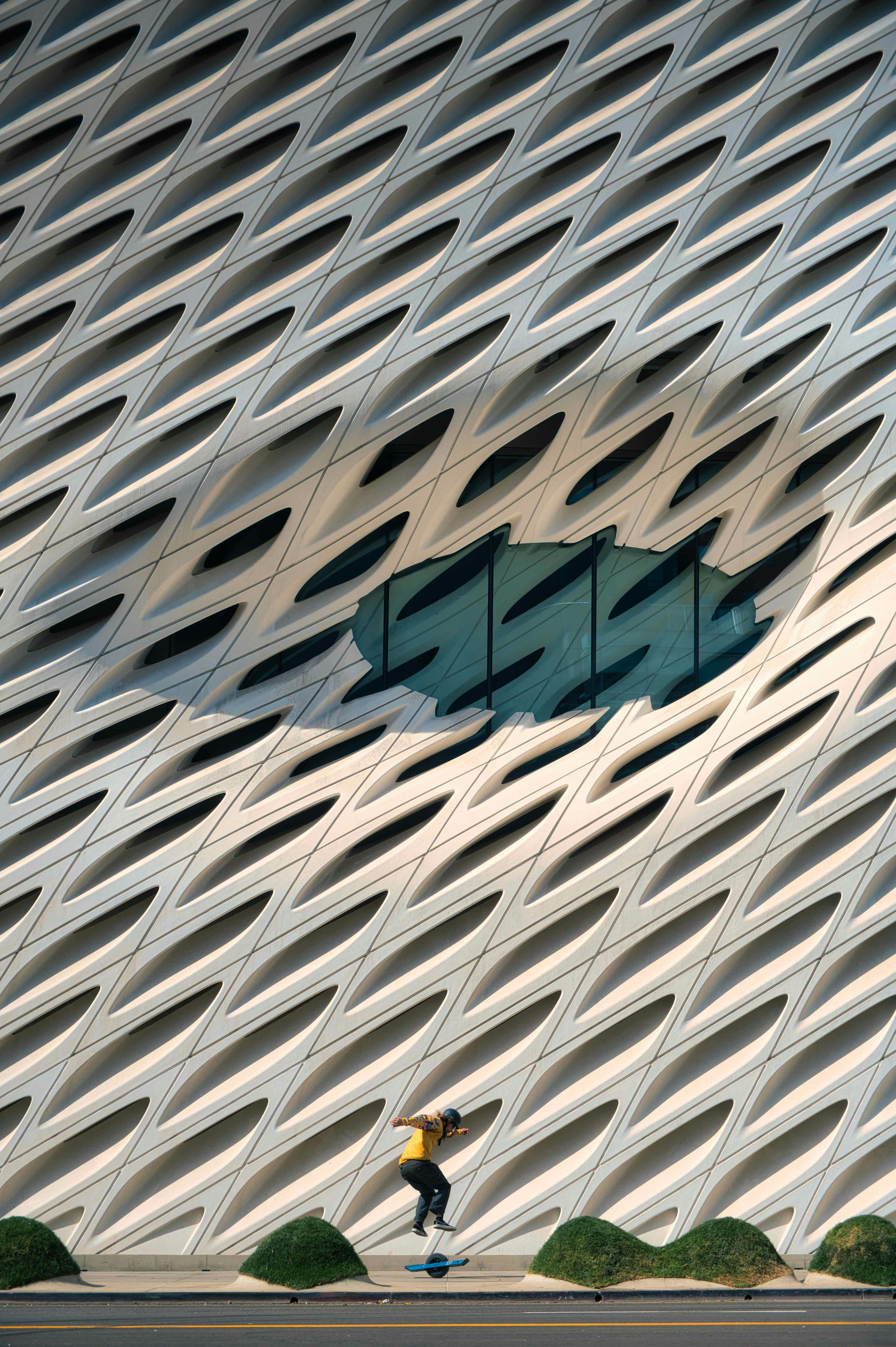 Skateboarder gliding along a textured facade with a striking window opening, showcasing the interplay of movement and architectural design.